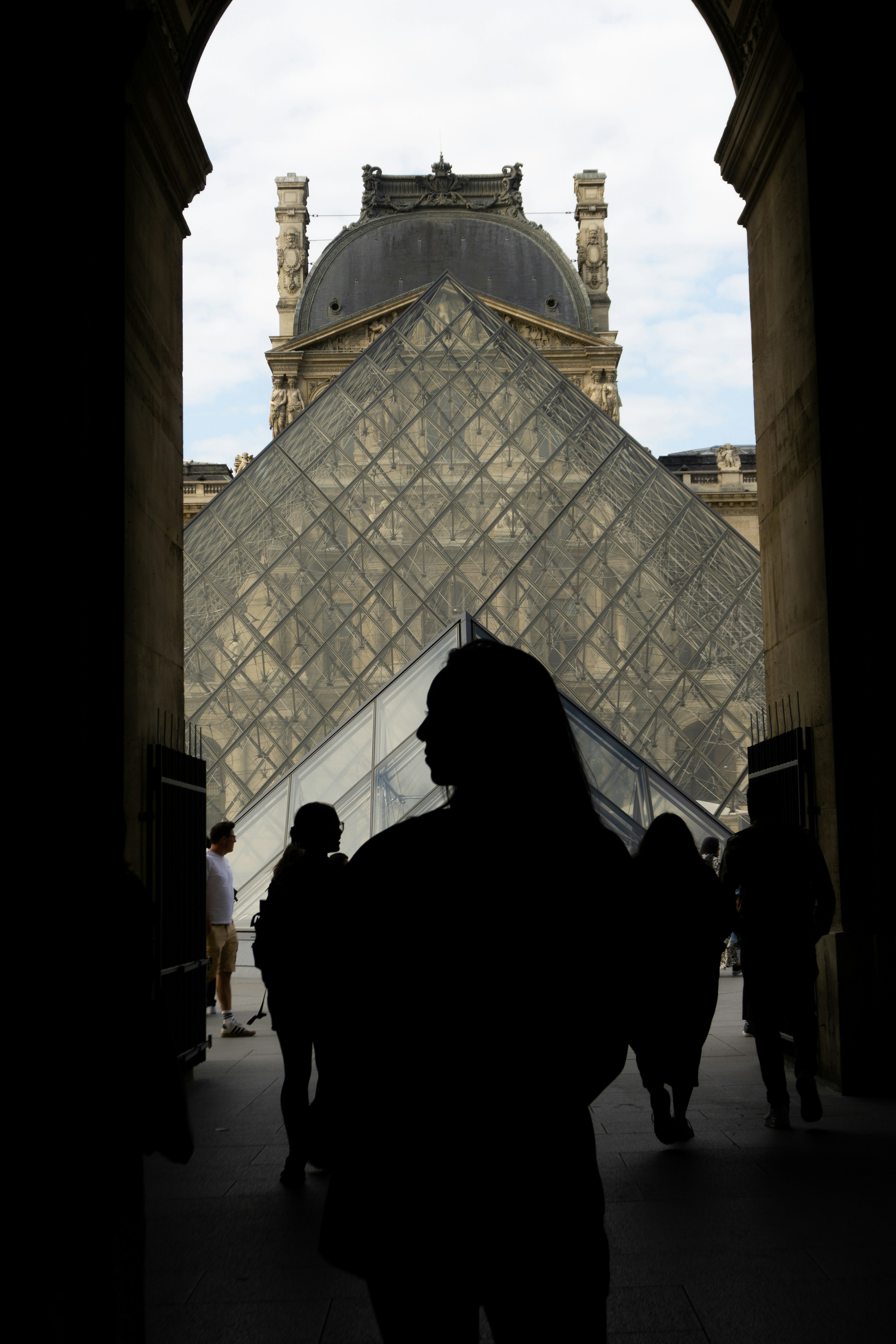 Silhouette Amid the Glass Pyramid: A Quiet Pause in Louvre Courtyard