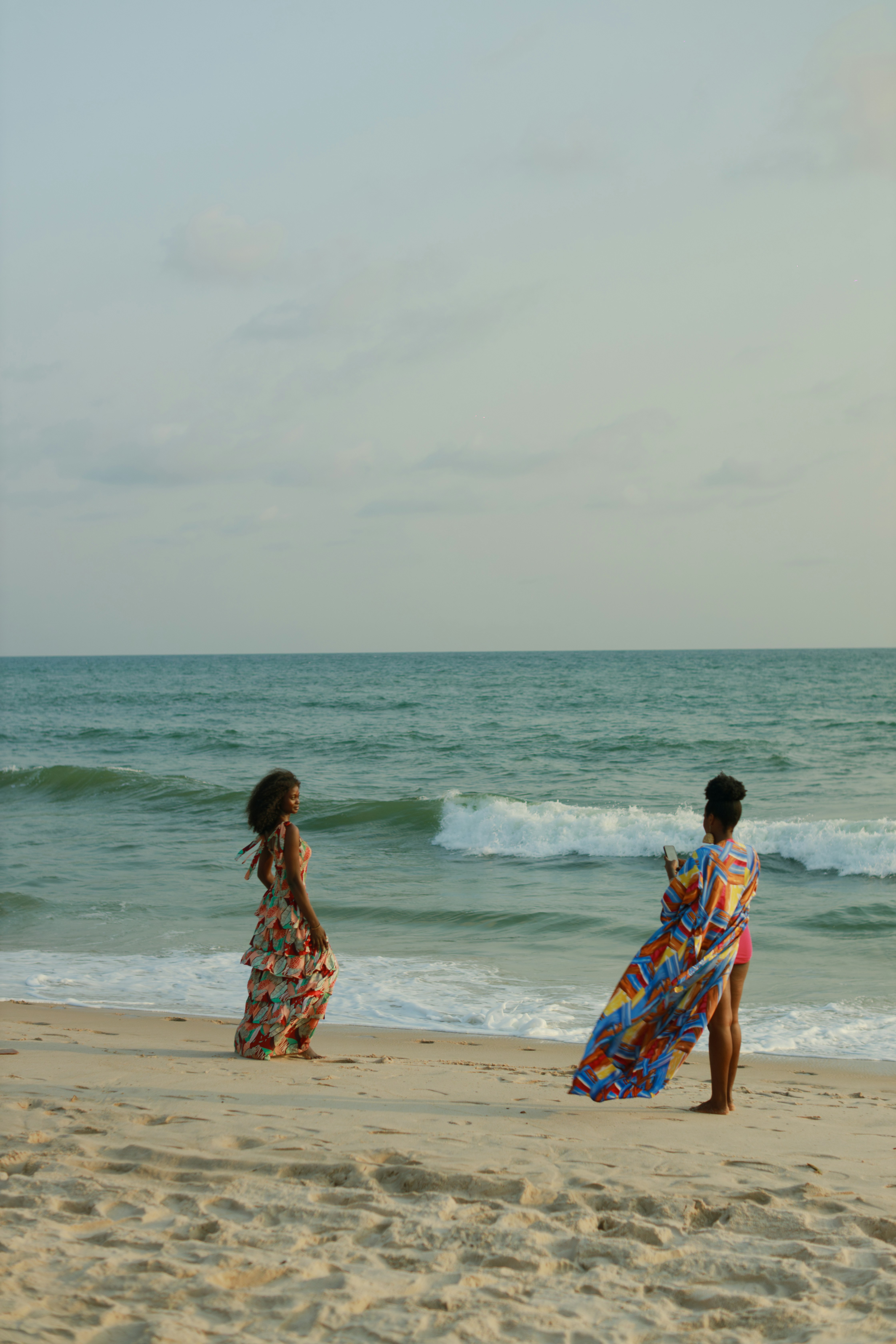 Beachside Meeting: Two Women in Colorful Draped Dresses by the Ocean