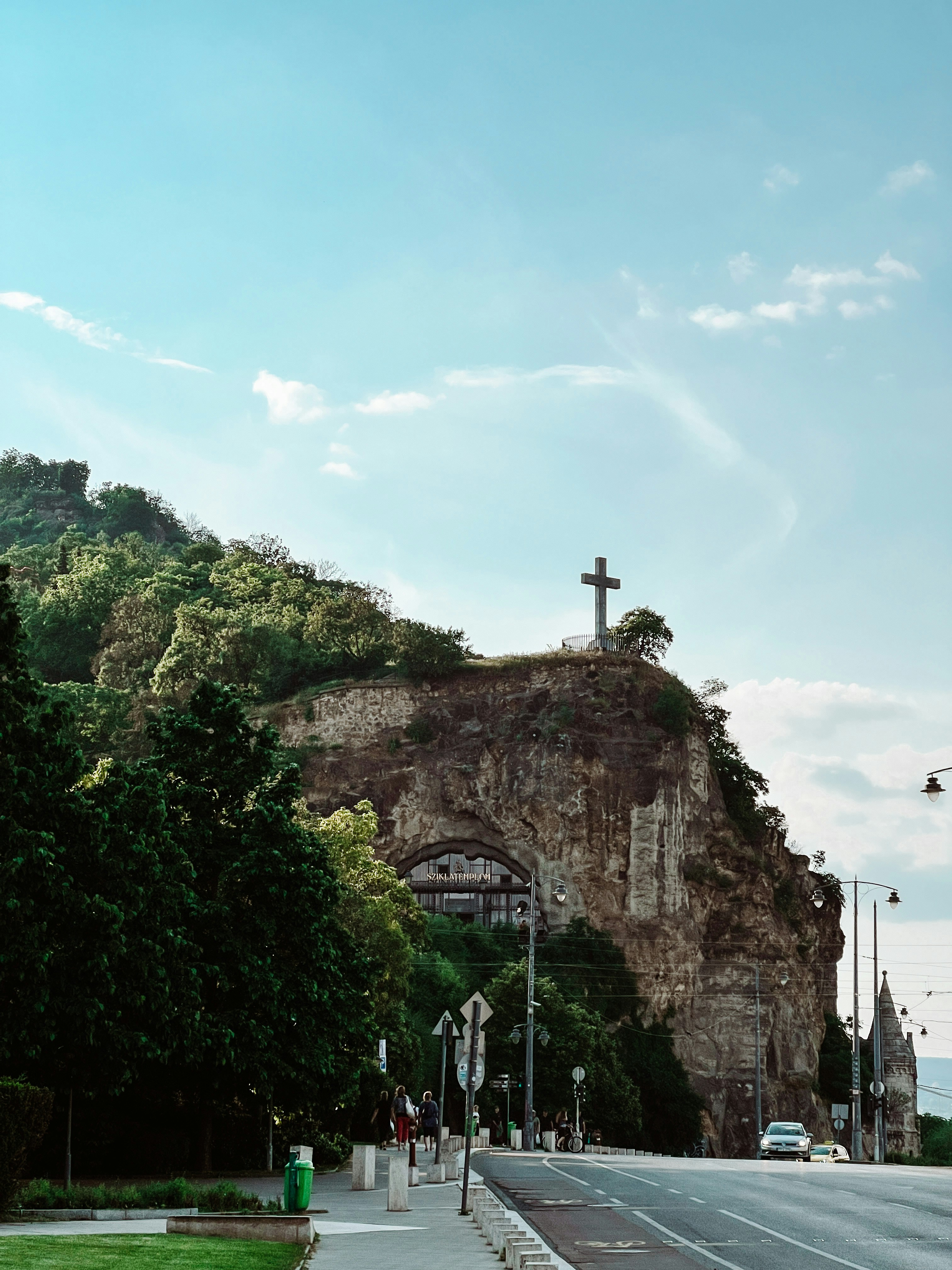 A large cross atop a rocky cliff with trees.