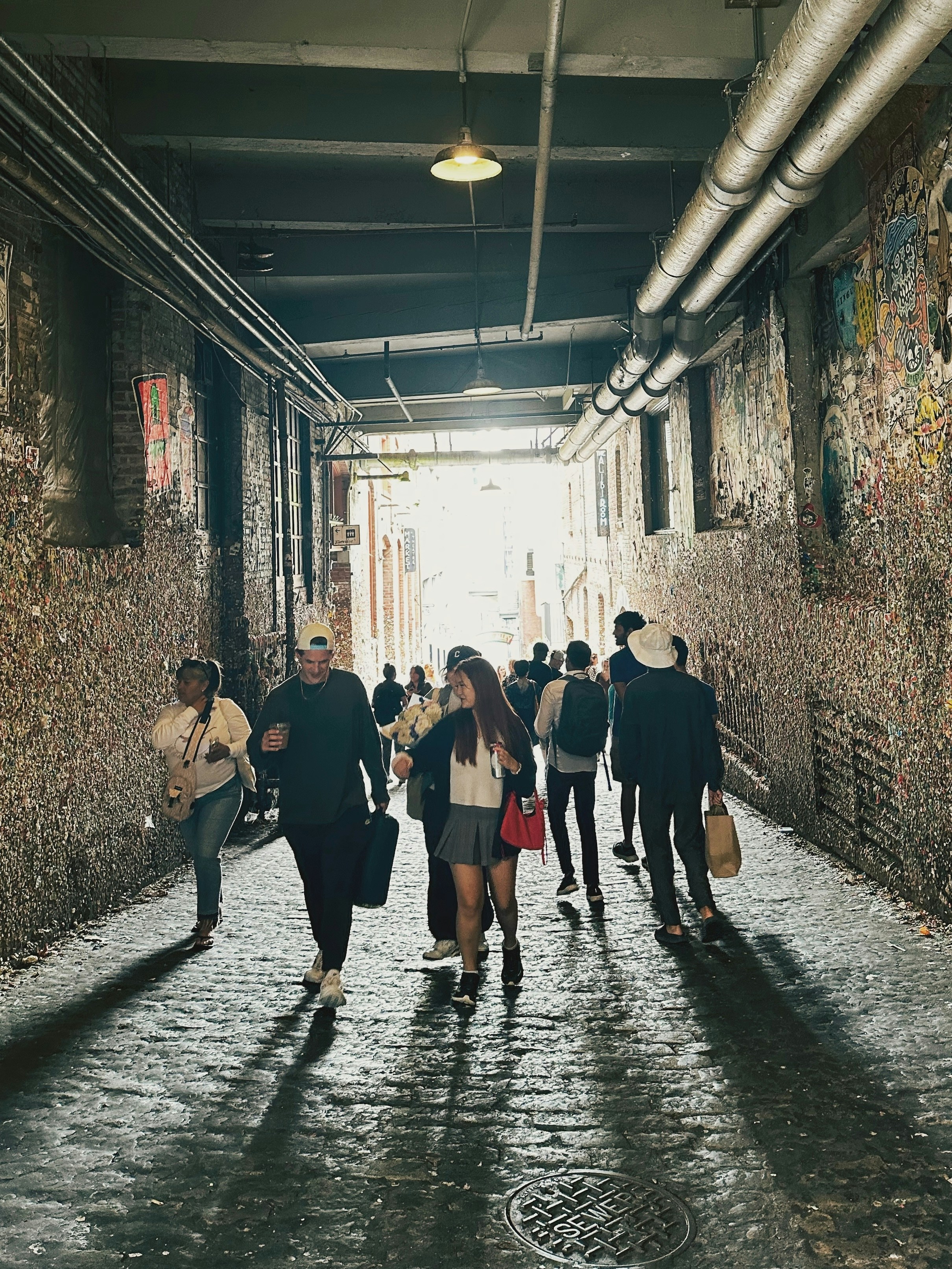 People walking down a cobblestone alleyway with brick walls.