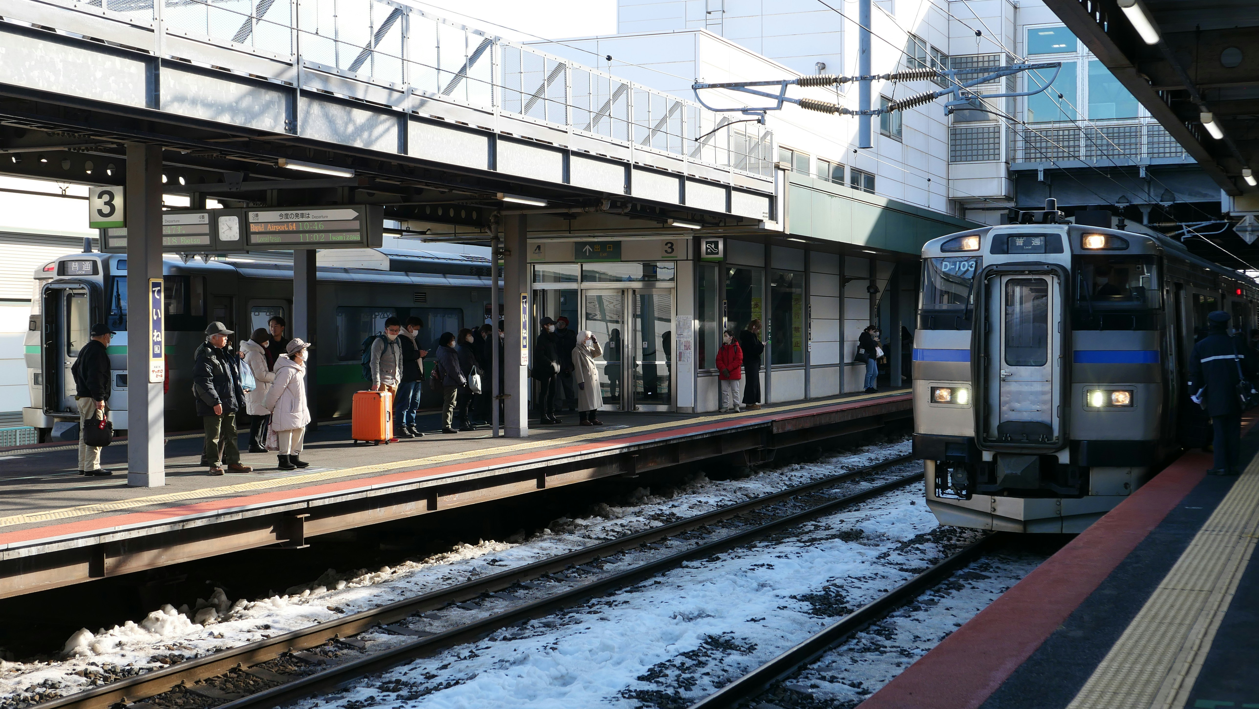Train at a snowy station platform with people waiting.
