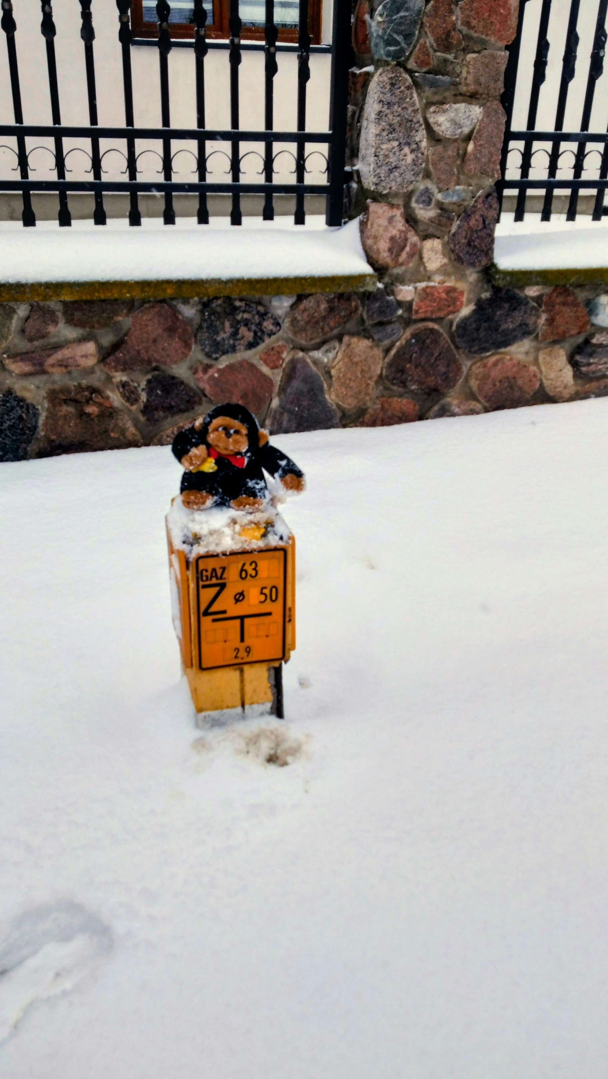 A stuffed monkey sits on a snow-covered marker.