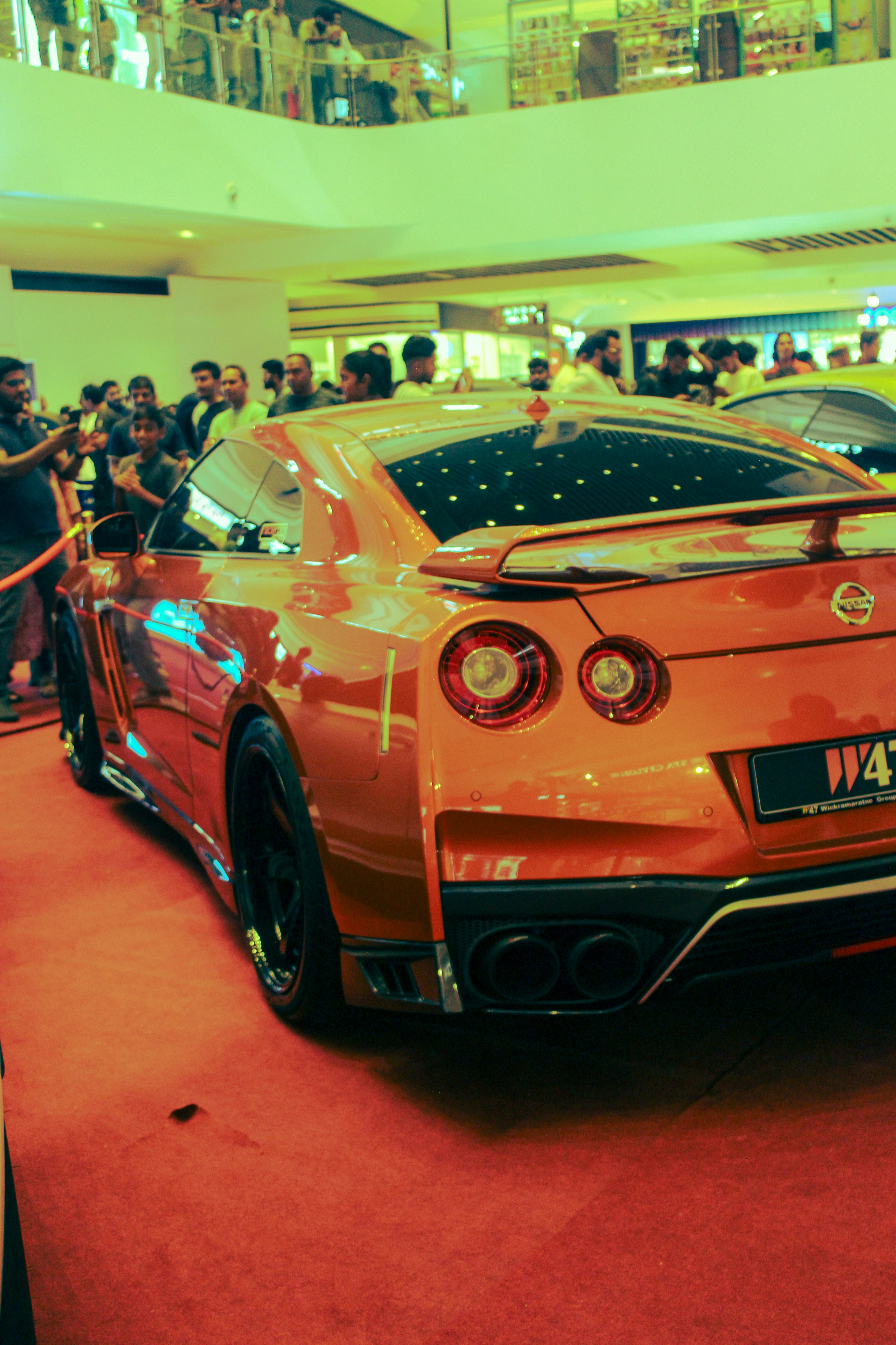 Orange supercar on display: glossy rear, crowd in a showroom