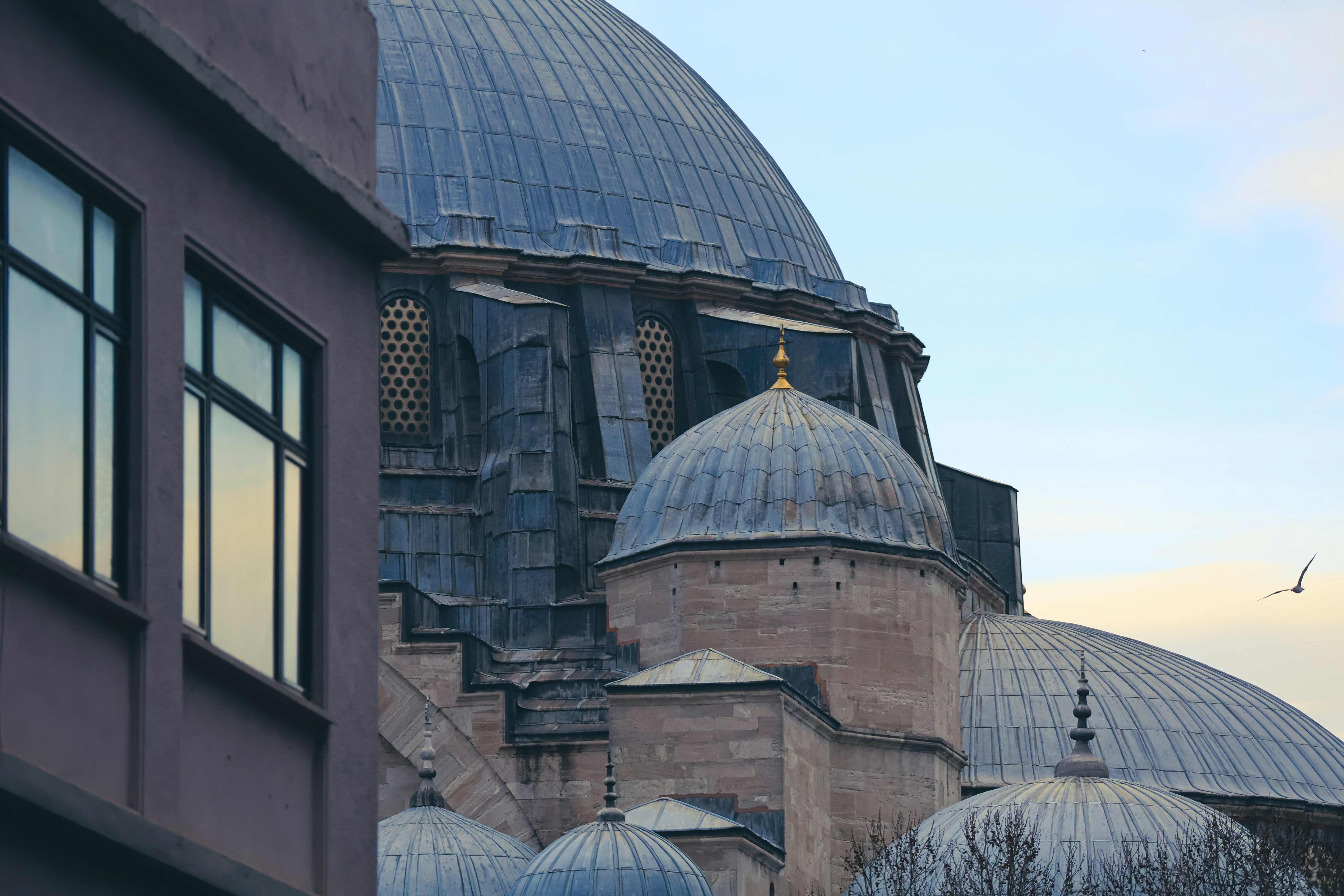 Architectural domes and stone work framed by a modern windowed building, showcasing overlapping historic and contemporary elements.