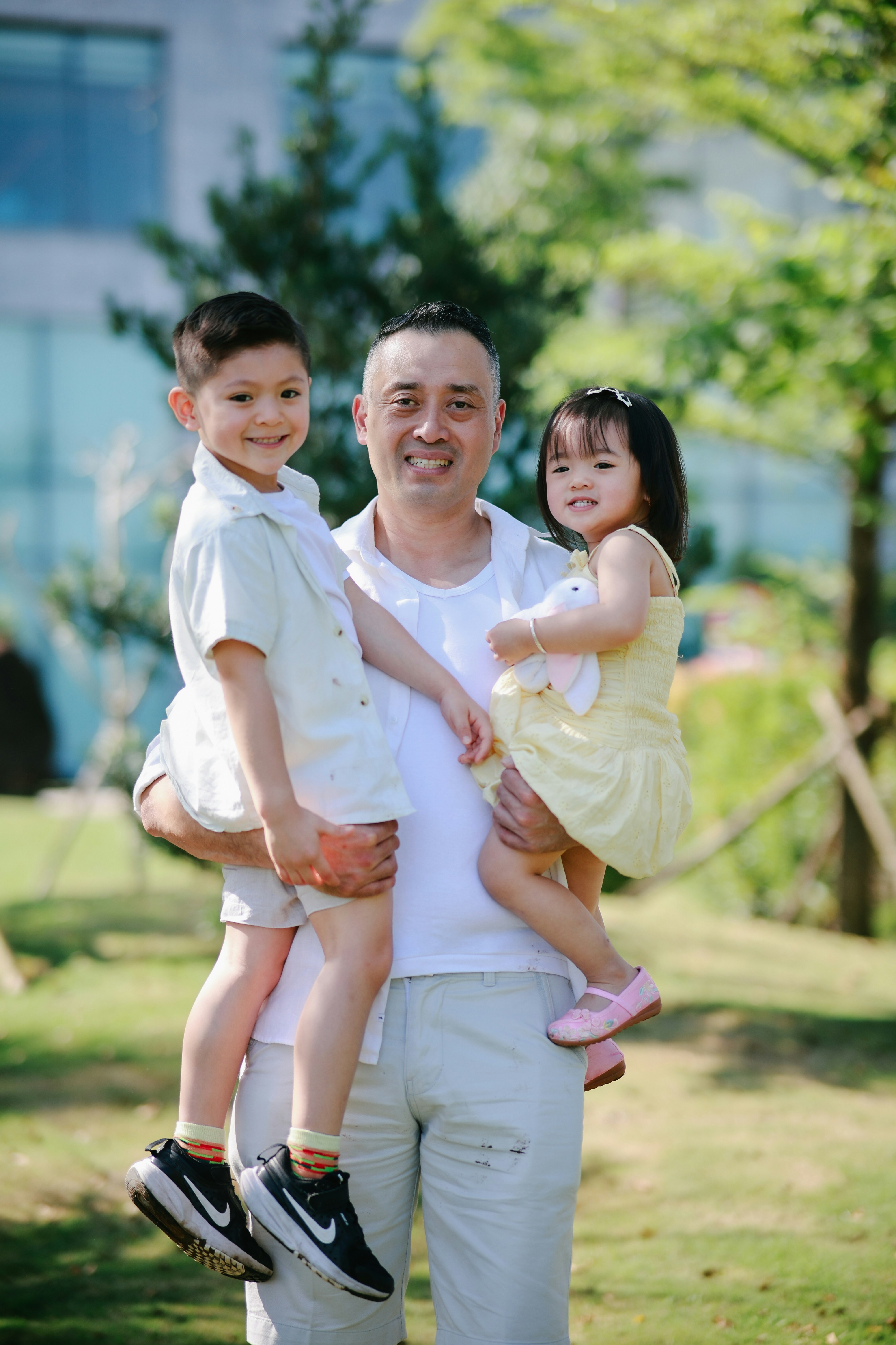 Dad Lifts Joy: A Sunny Moment with Two Little Climbers
