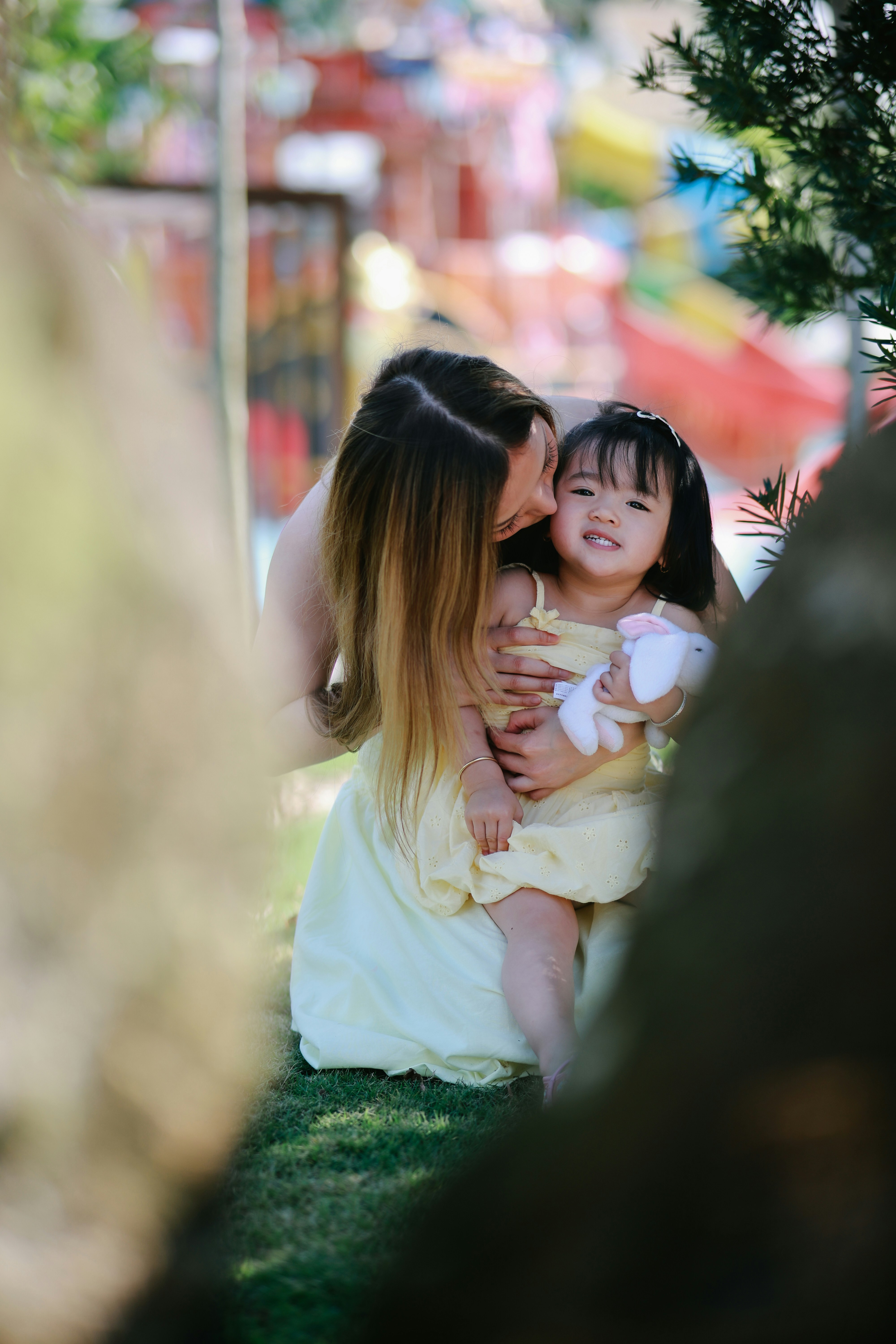 Mother and child in a sunlit park embrace under colorful festival reminders
