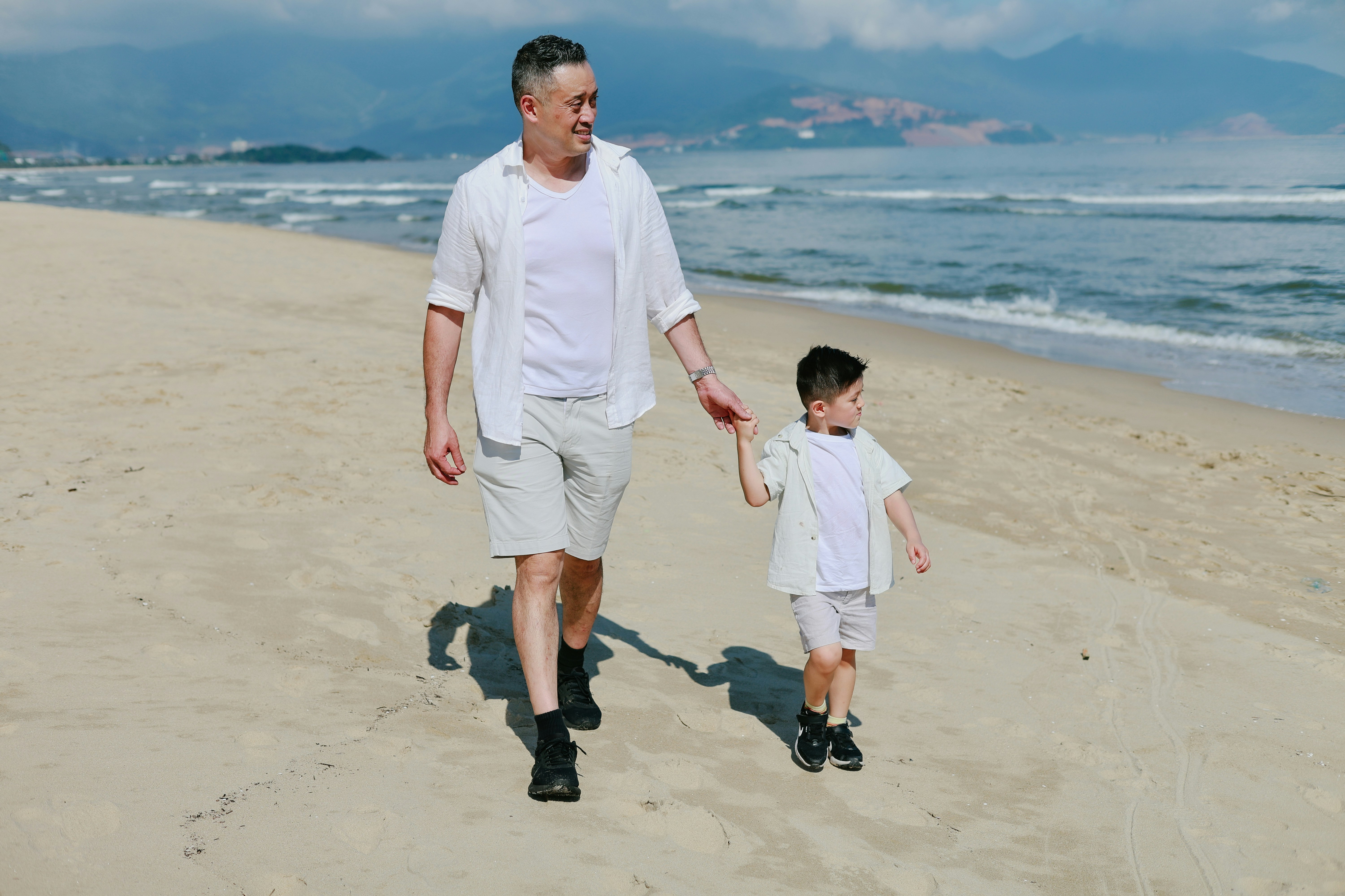 Father and Son Walk Hand in Hand Along Sunlit Seaside