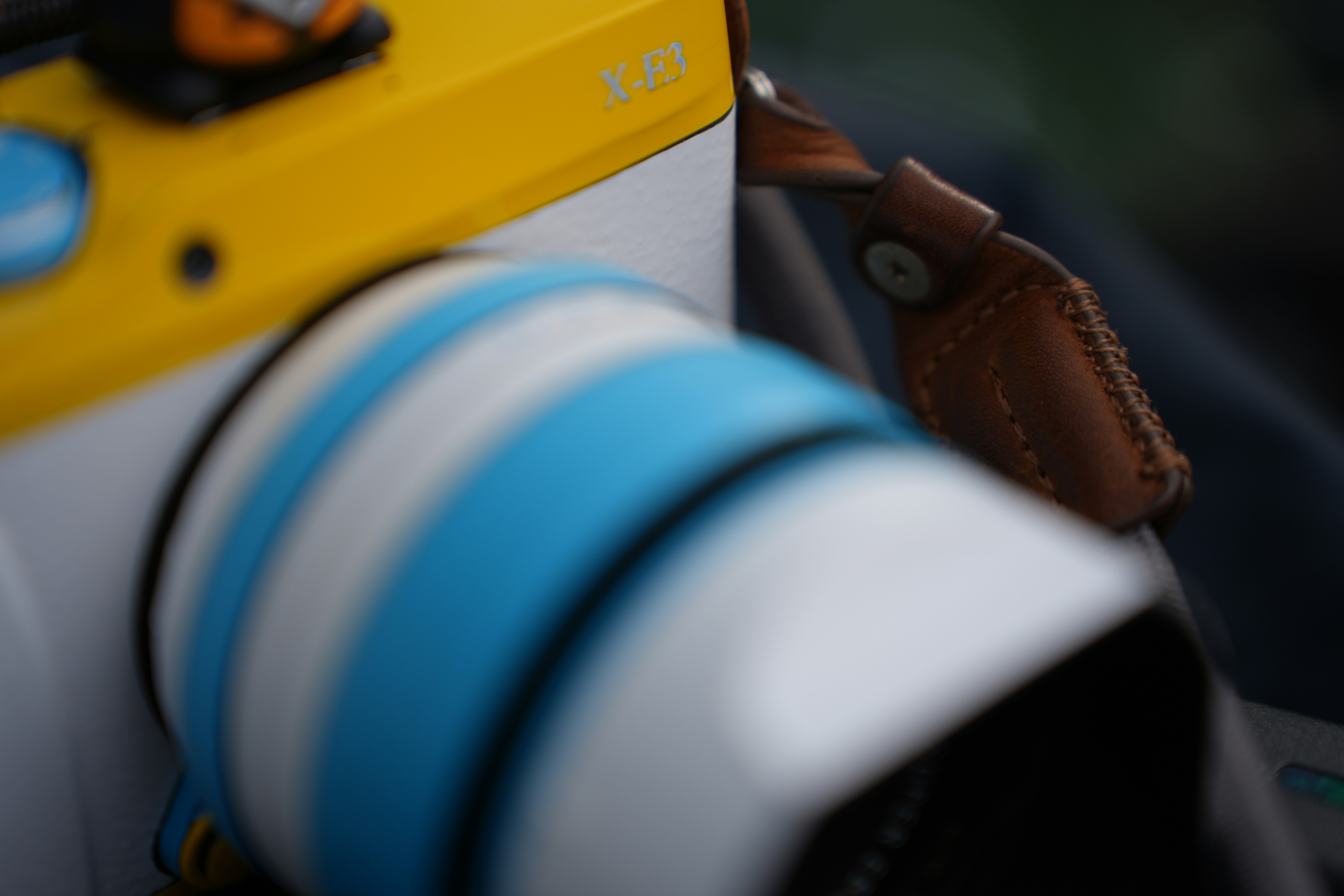 Close-up of a compact 35mm-style camera with a teal lens and brown strap