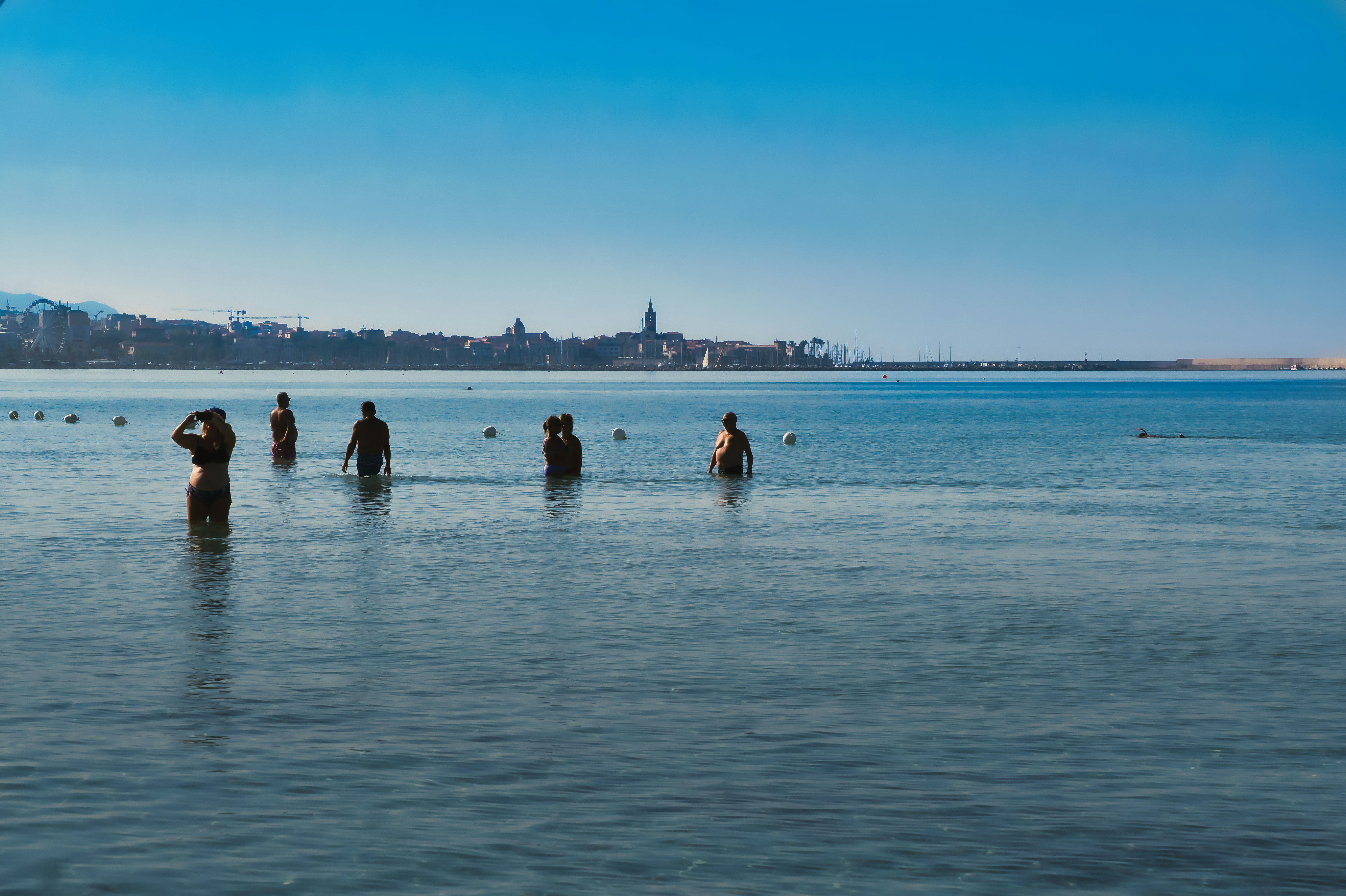 Coastal Silhouettes: Figures in Calm Tide at Distant Town Horizon