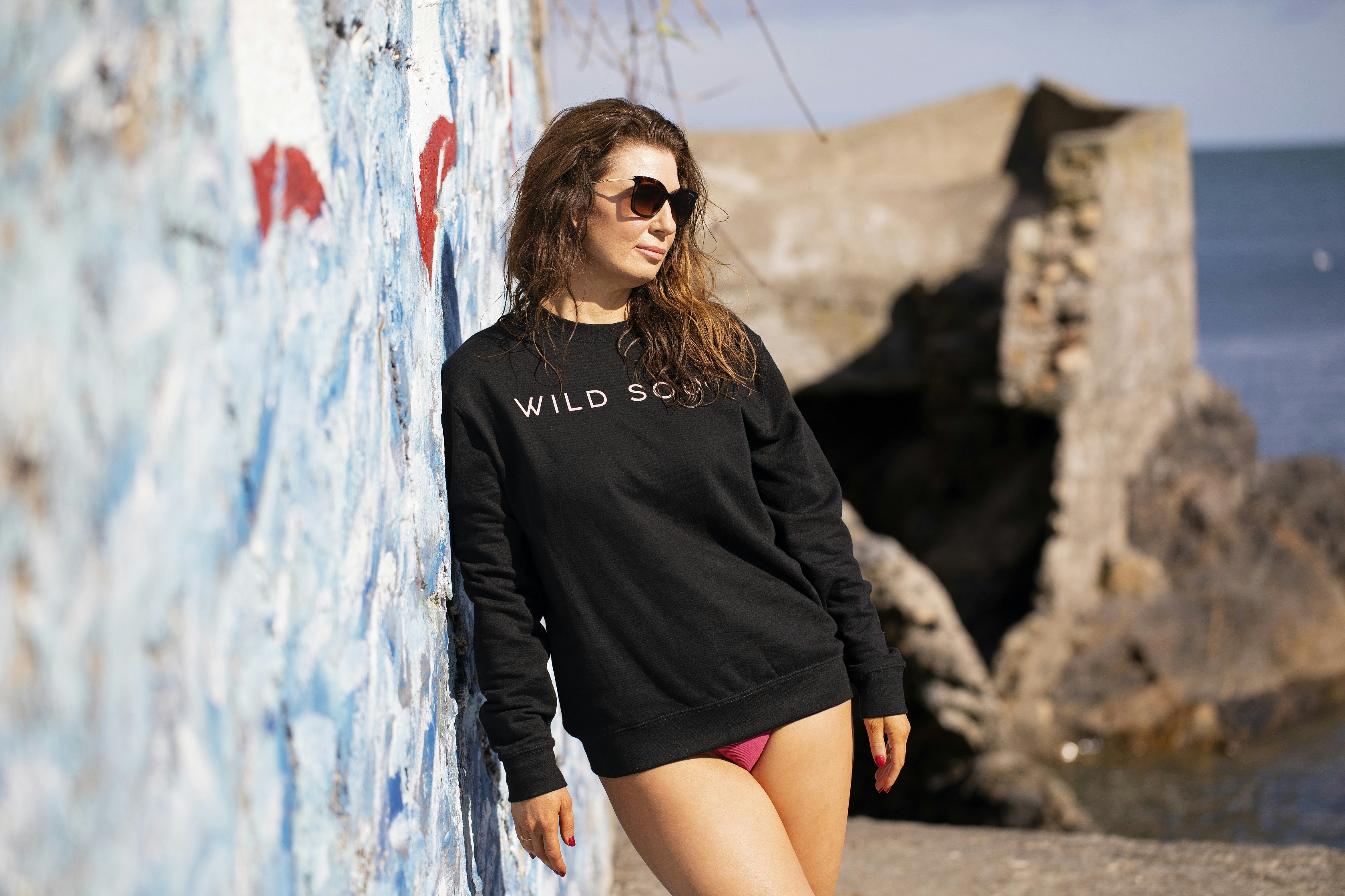 Woman leaning against a graffiti wall by the sea