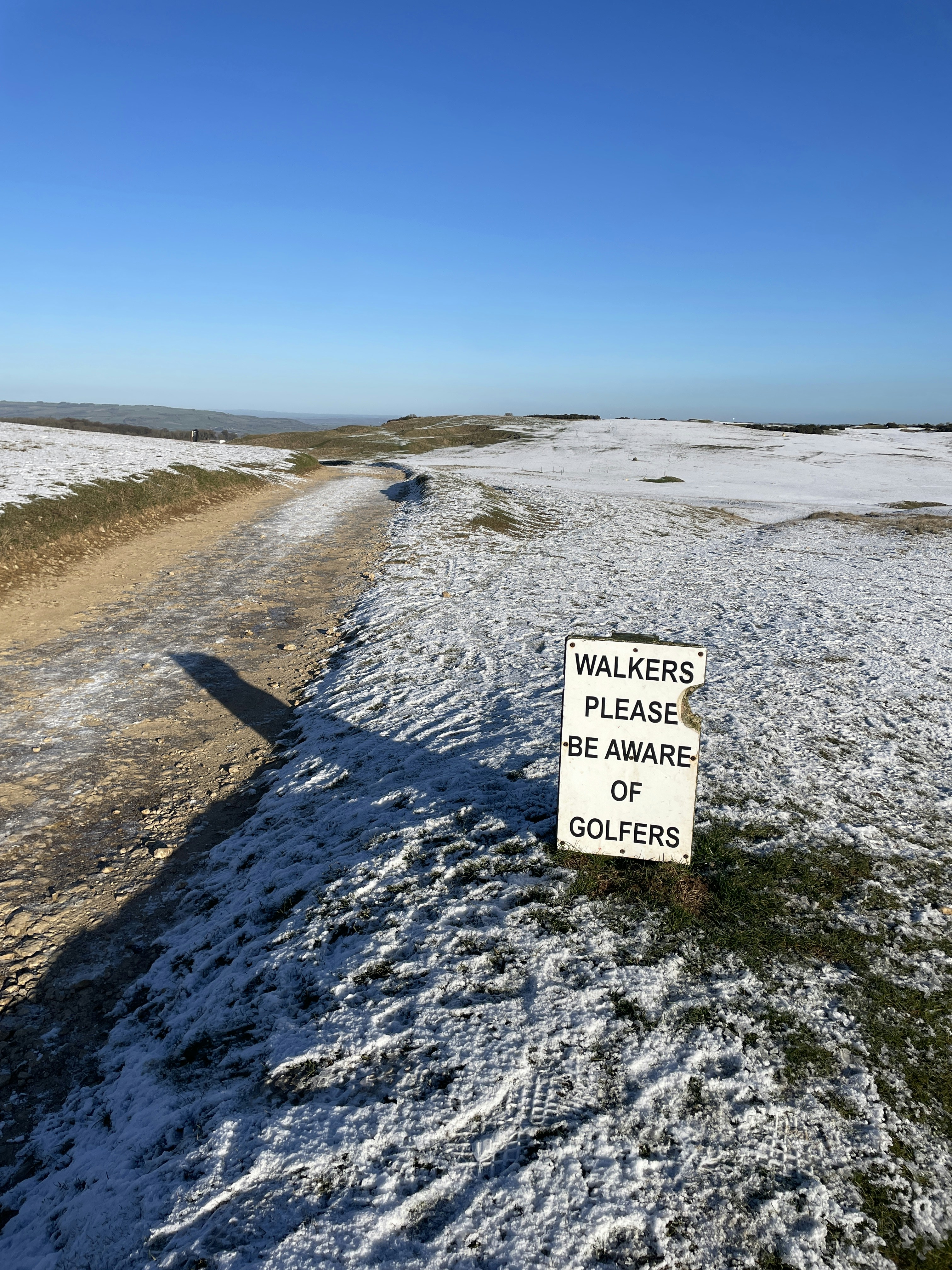 Snow-dusted path toward the distant coastline with a roadside warning sign