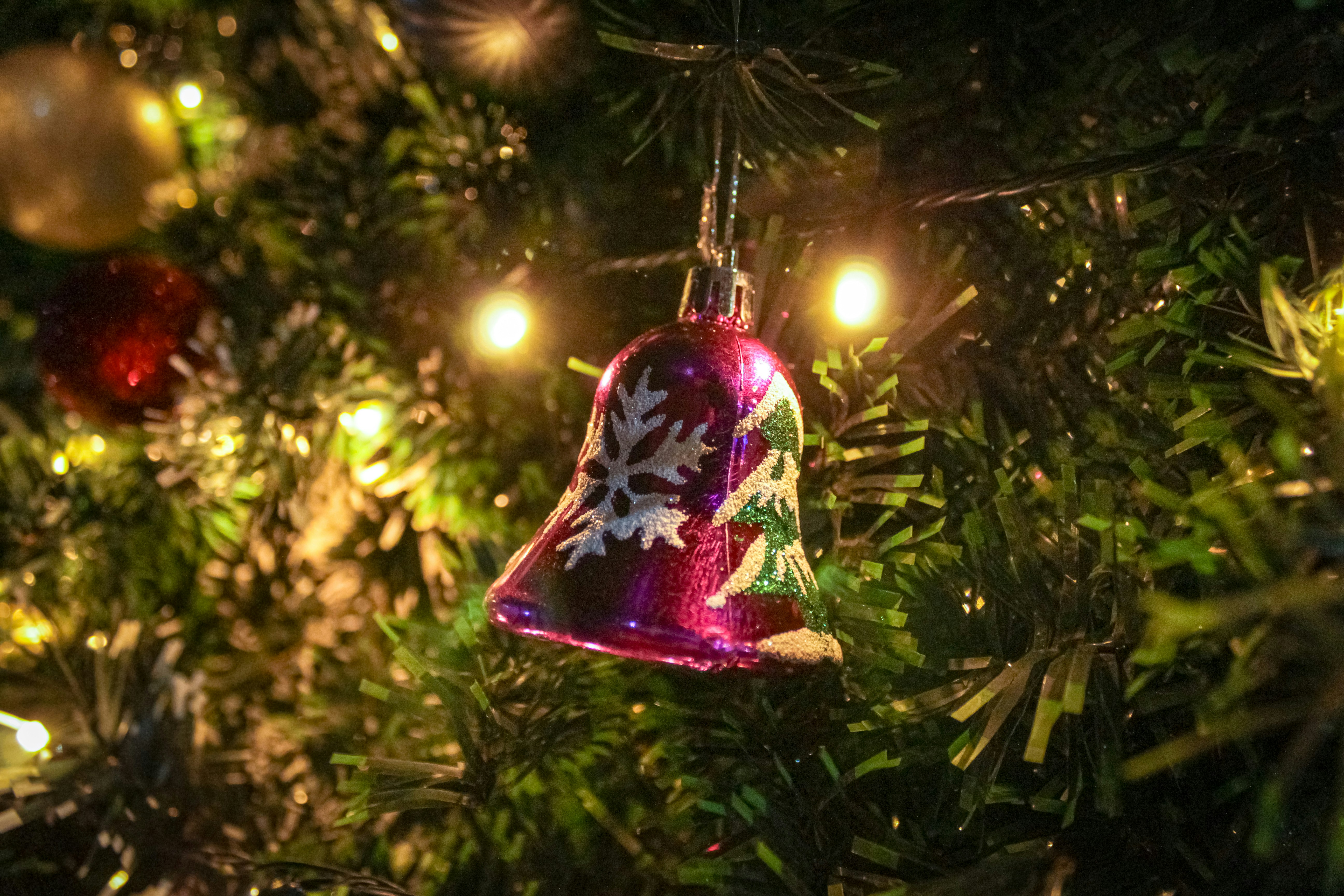 A Glittering Bell Ornament Weighs Down a Branch of Warm Christmas Lights