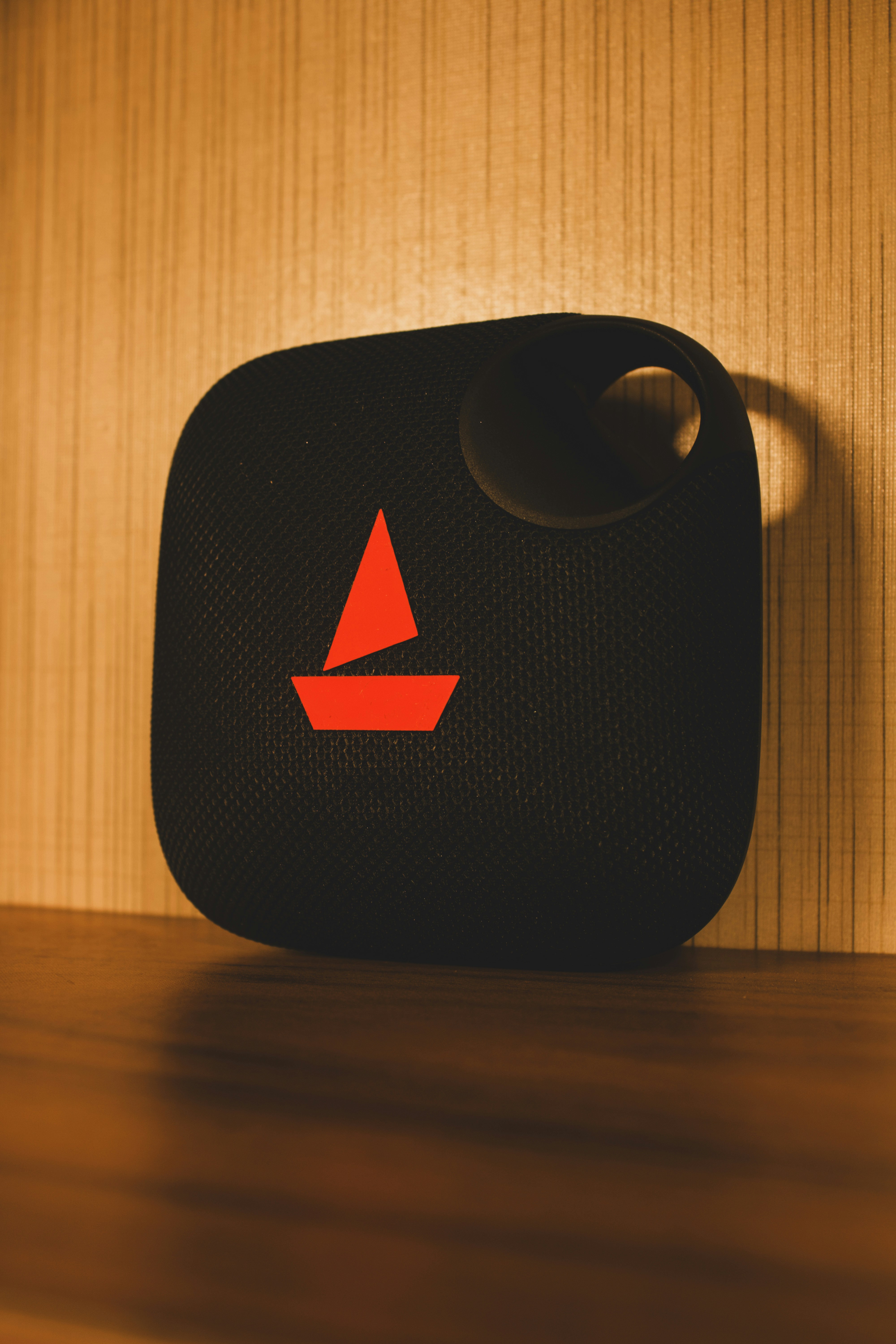Compact Speaker with Red Logo Leaning Against a Wooden Panel