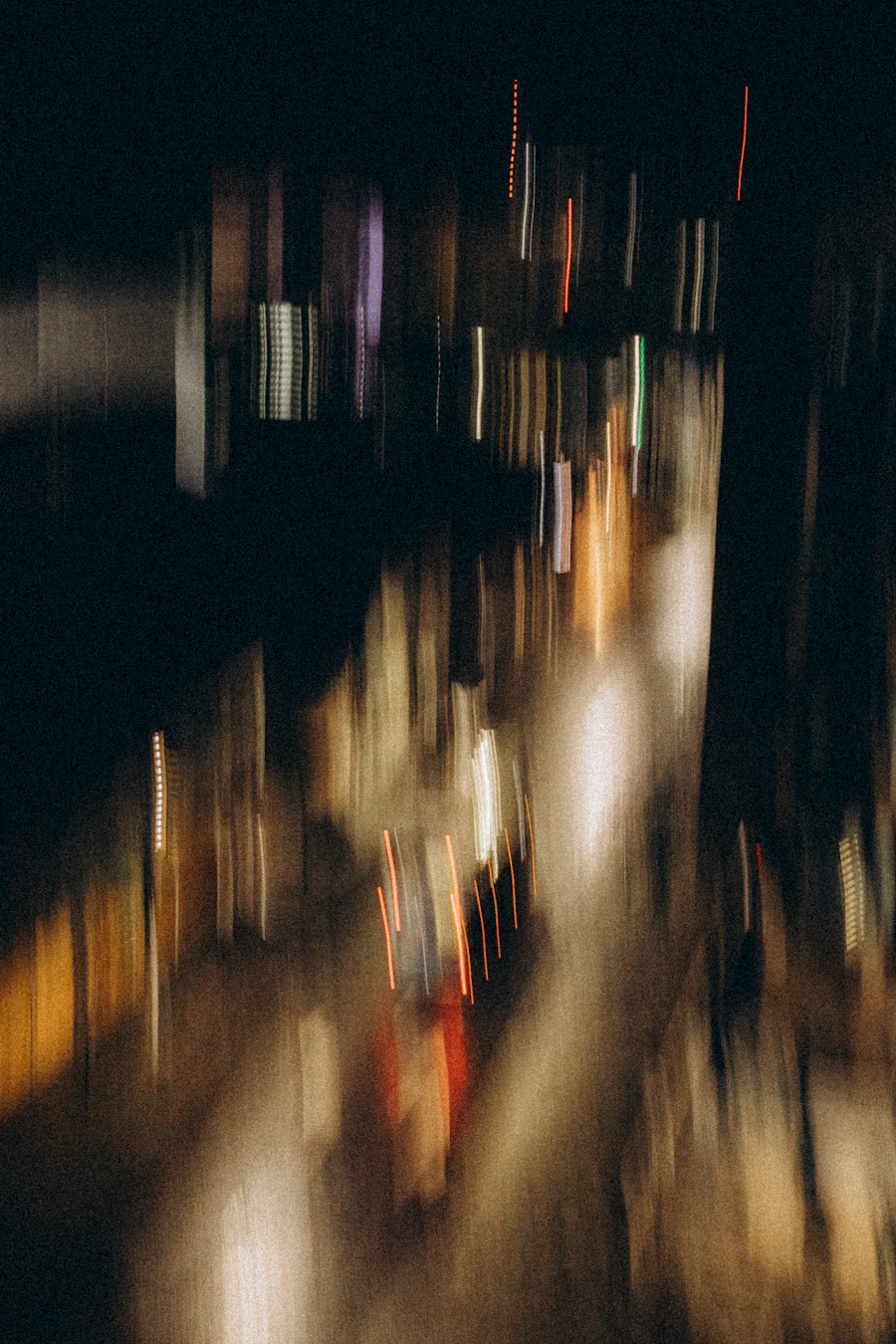 Blurred urban nightscape with streaks of warm lights; abstract motion creates painterly vertical ribbons across a dark street.