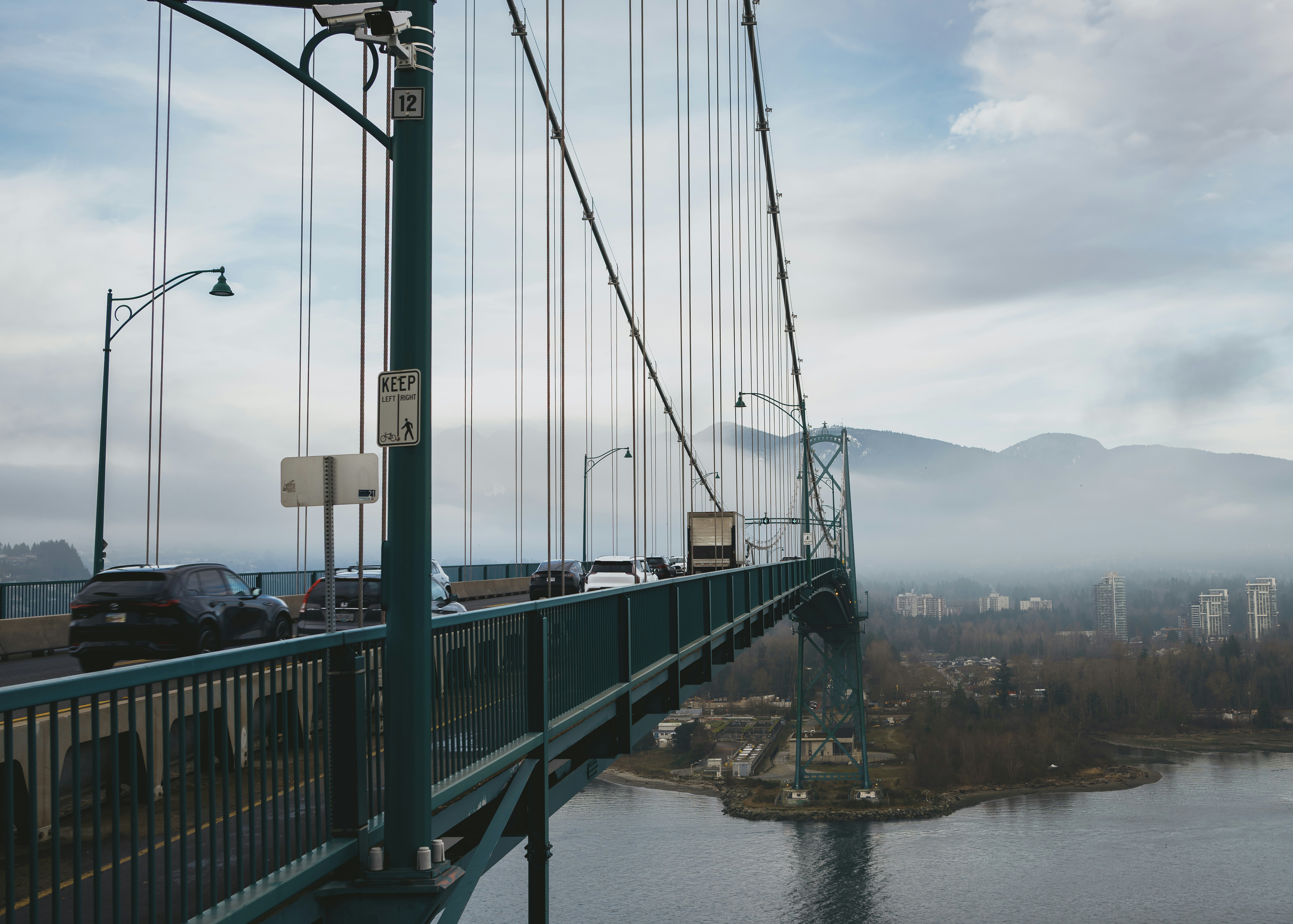 Mid-Span of a Verdigris Suspension Bridge Over a Calm River