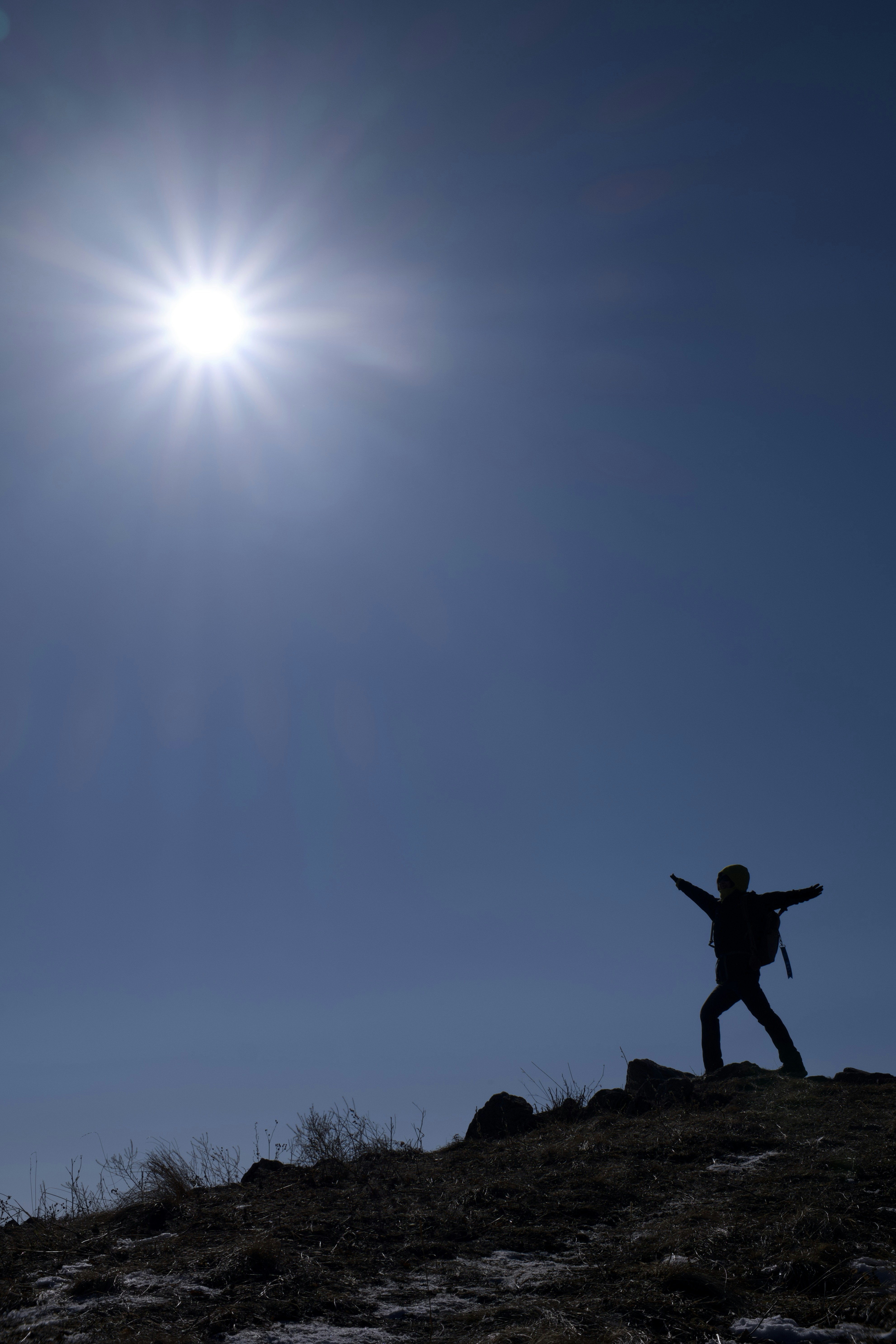 Sunlit Summit: Silhouette with Outstretched Arms on Dawn’s Slope