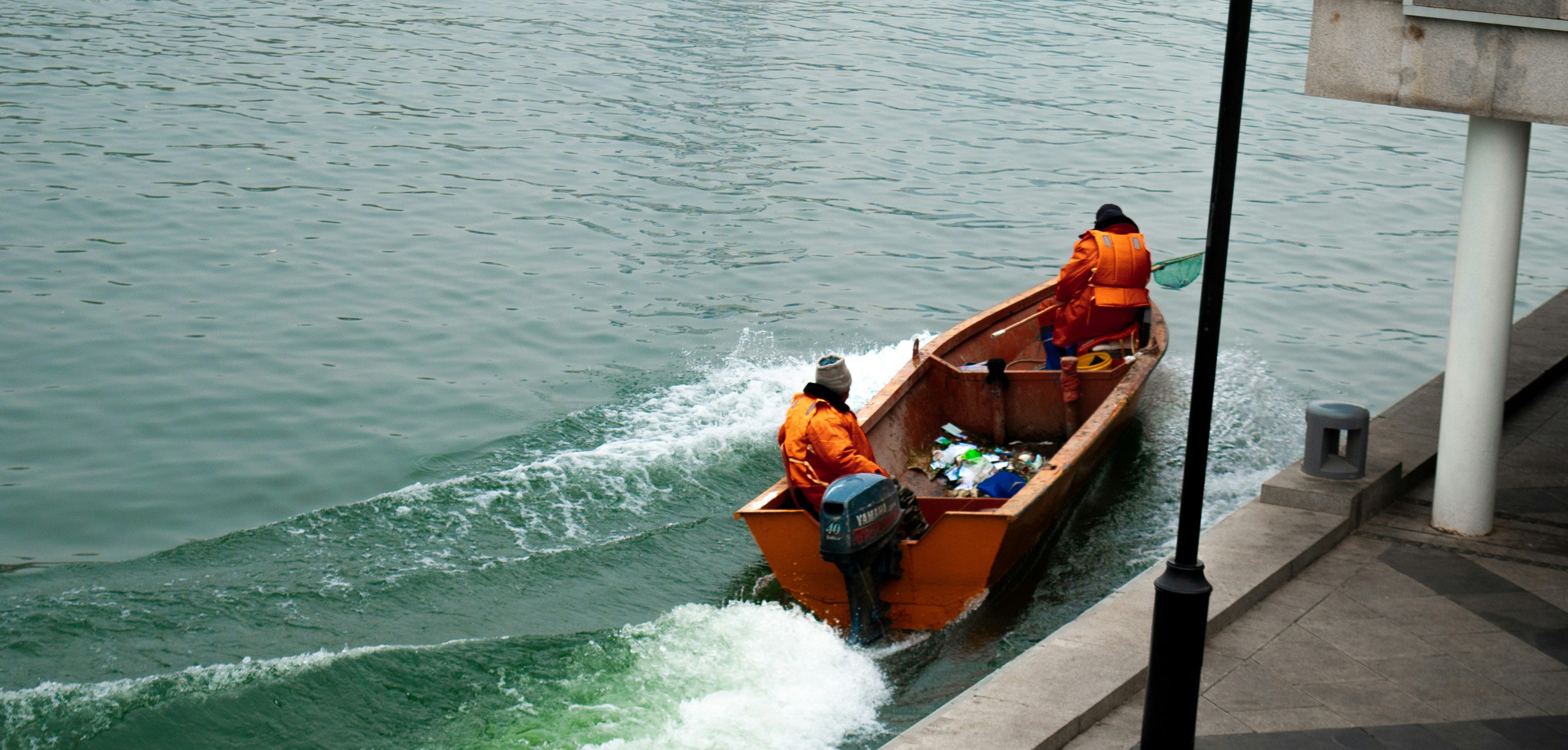 Orange Boat in Transit: Crew at Work Along a Concrete Dock