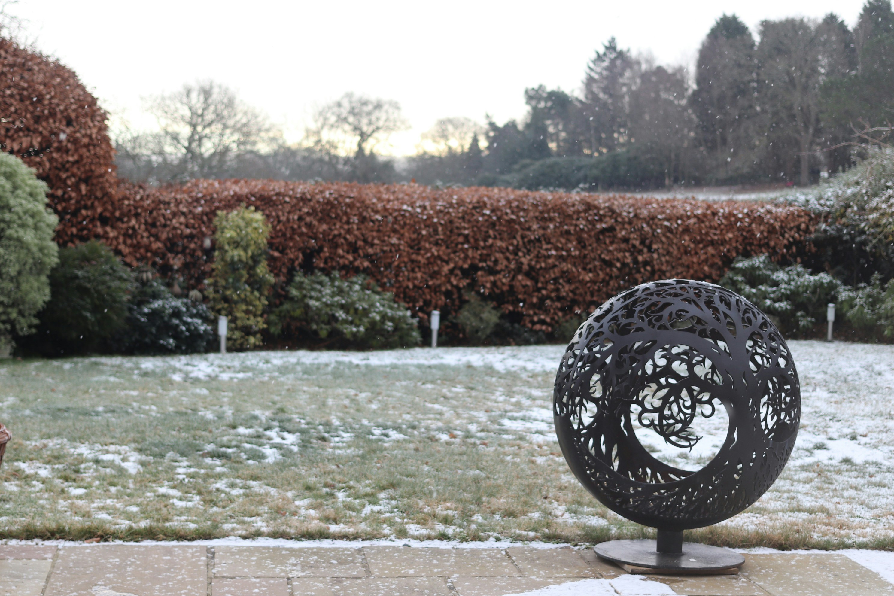Scrollwork in the Snow: A Circular Metal Sculpture Framed by Winter Garden