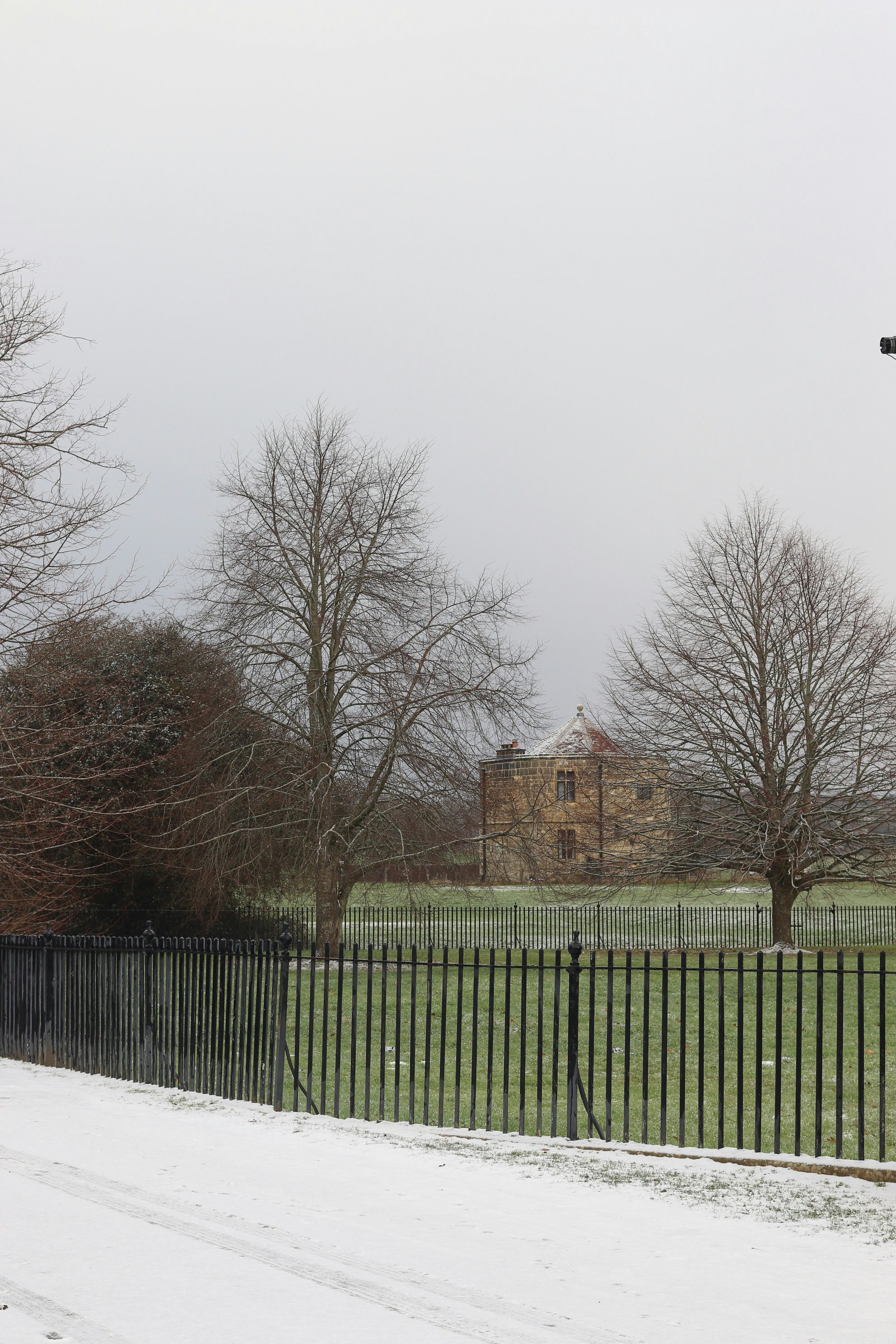 Snow-lined Grounds and Quiet Manor: A Winter Fence-and-Tree Scene