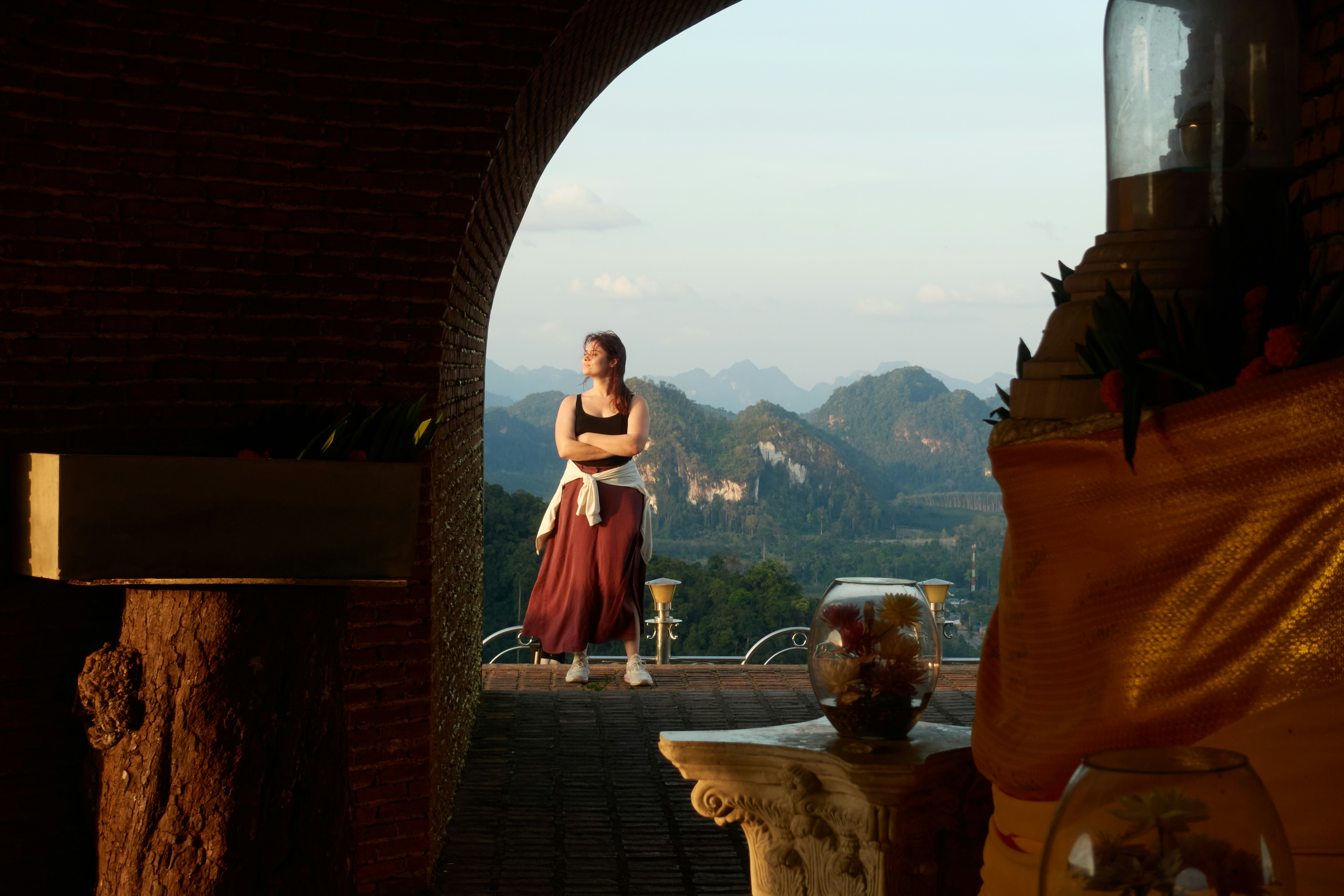 Figure in a sunlit terrace framed by ancient arch and distant mountains