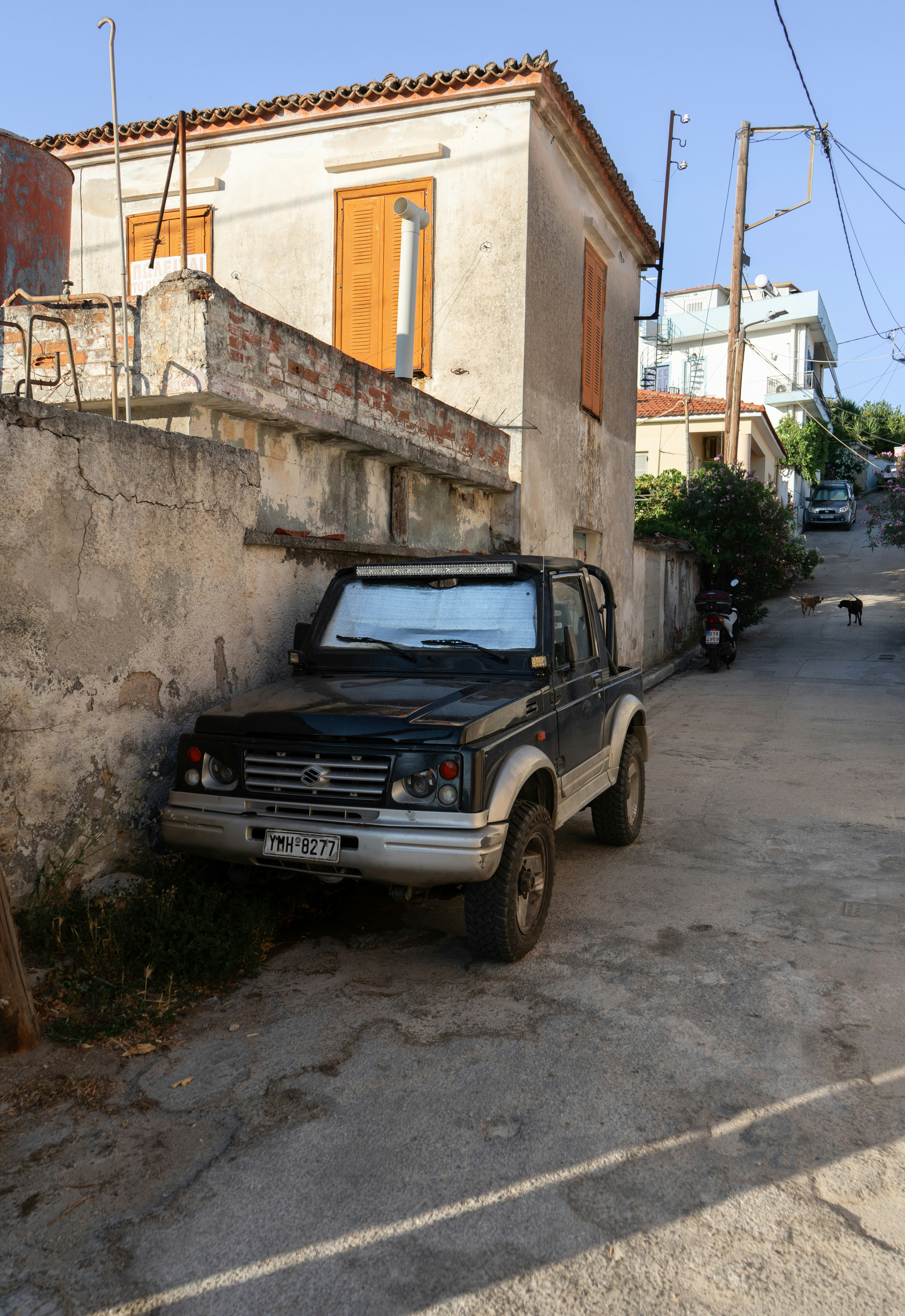 Sunlit Urban Drive: A Weathered SUV Rests by a Narrow Thessalonian Street