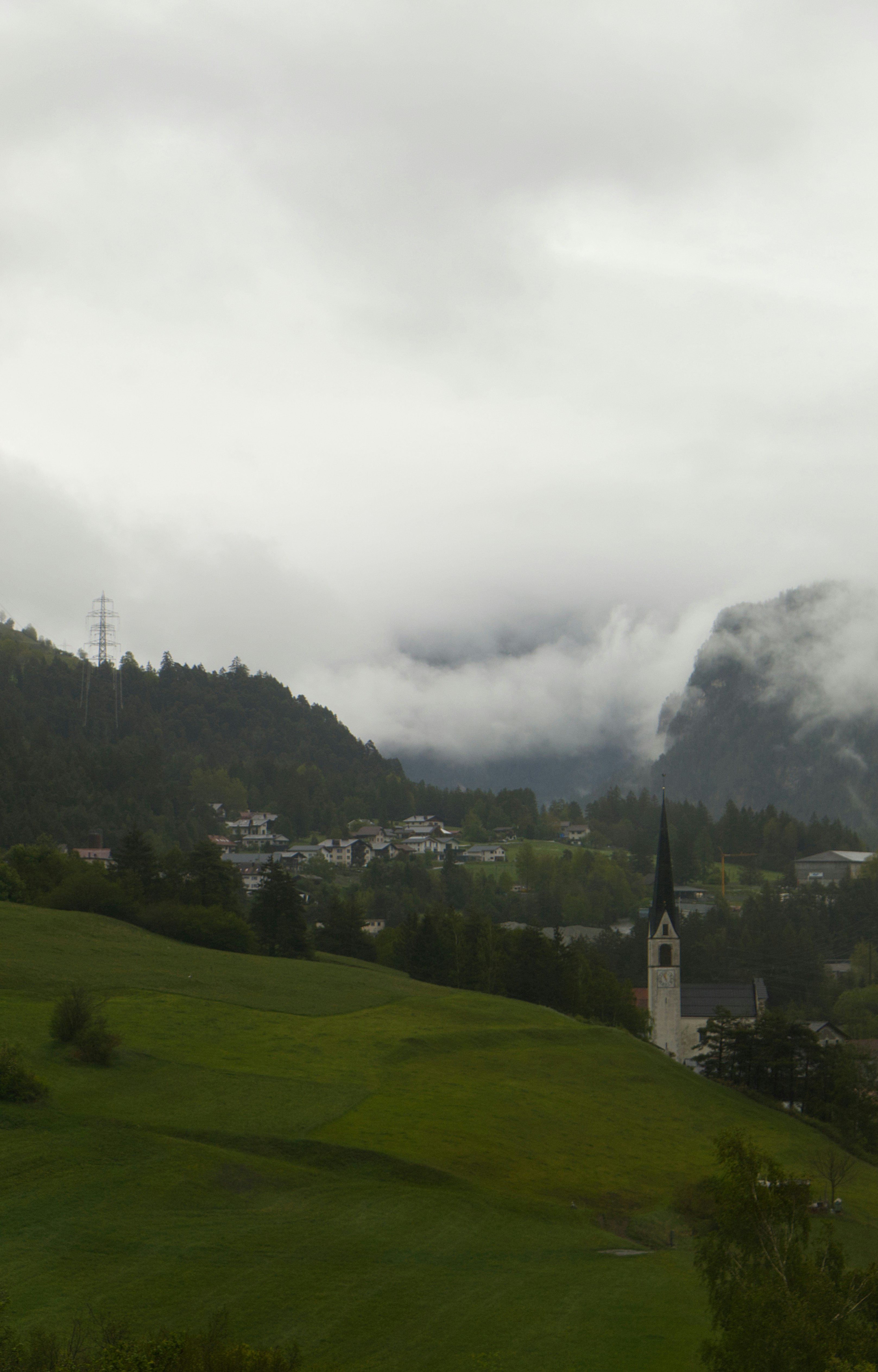 Village steeple rising above rolling green hills beneath misty mountains