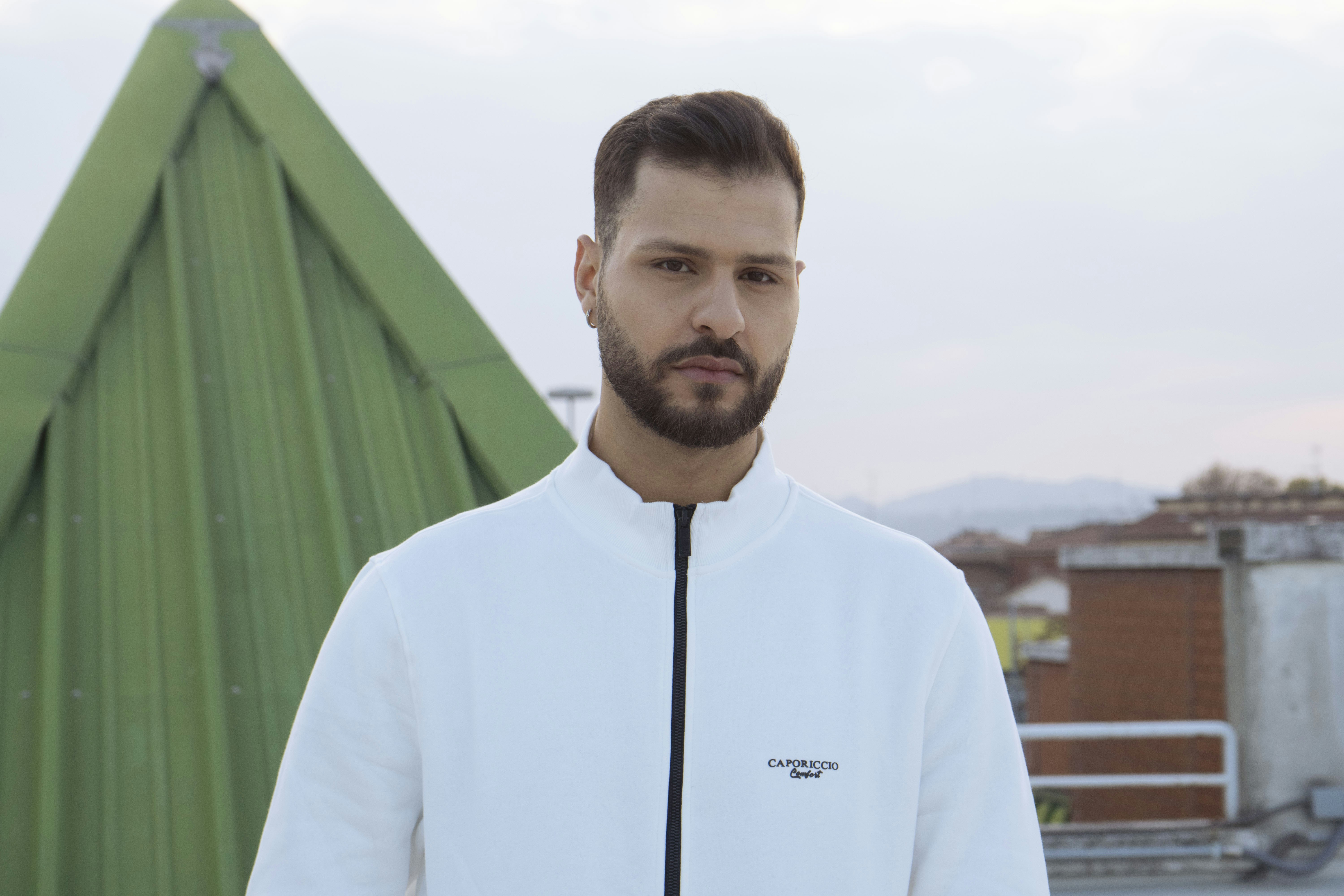 Centered groomed portrait against a green angular backdrop on a rooftop