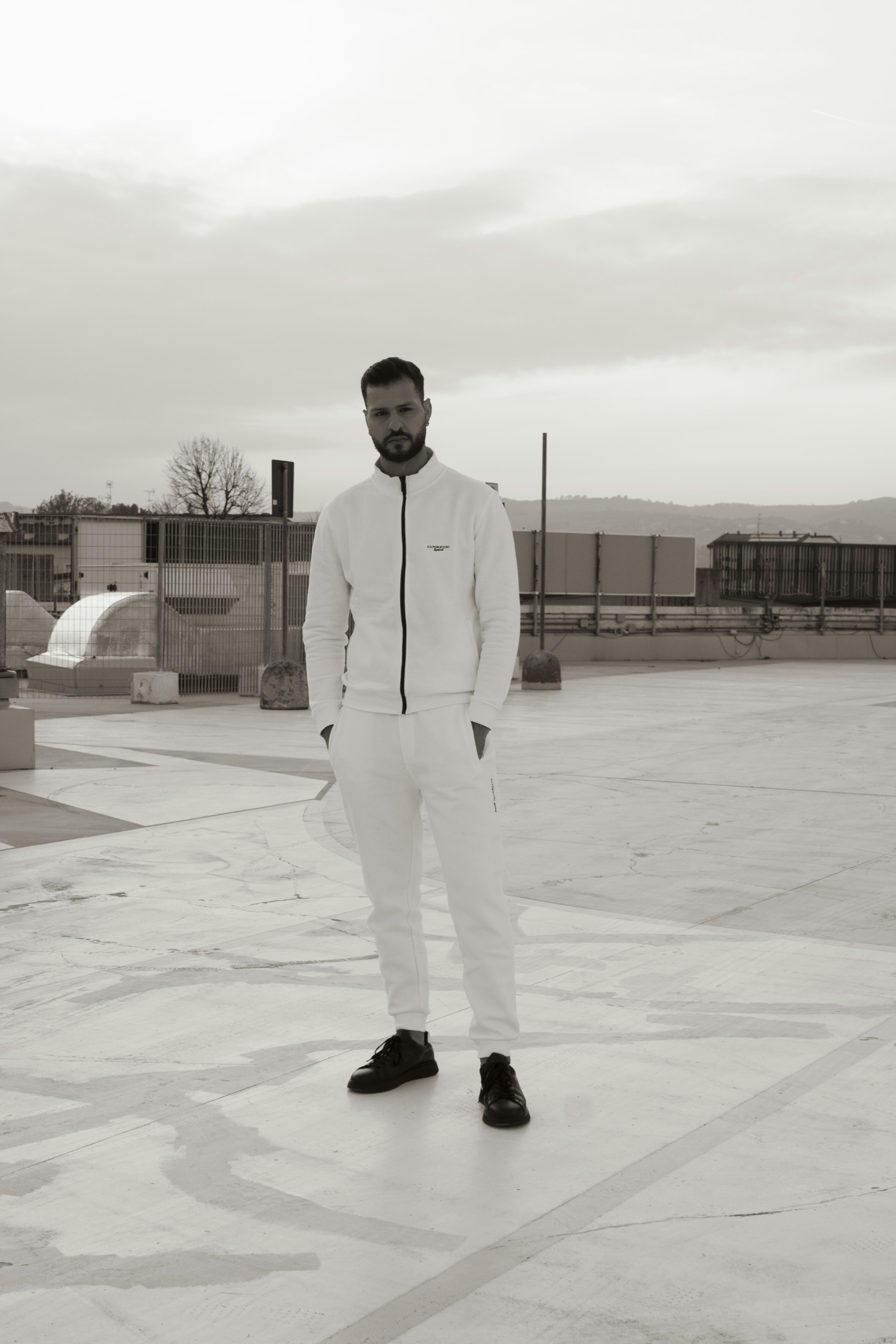 Monochrome rooftop portrait: a poised man in white tracksuit stands under an expansive sky