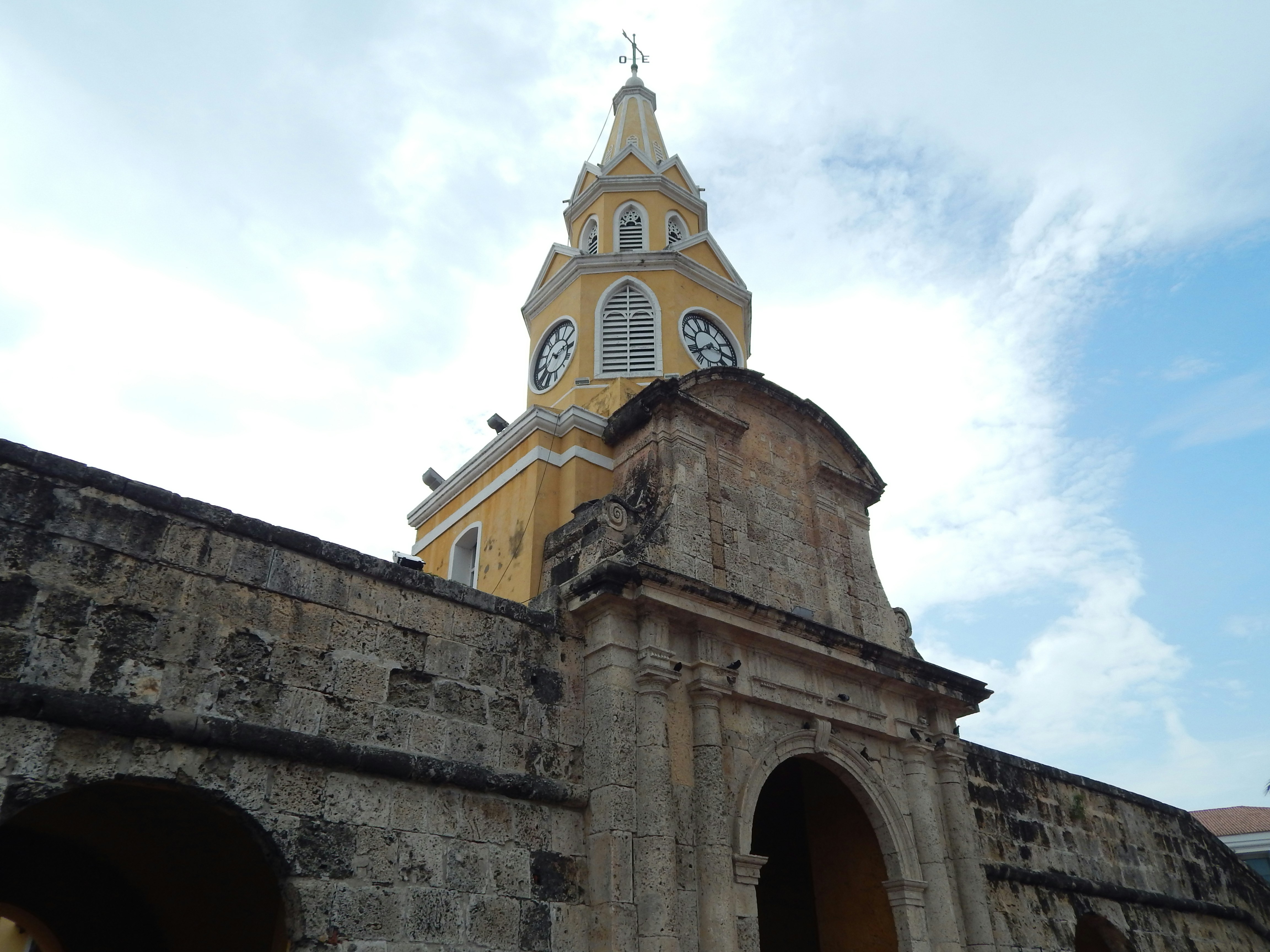 Tall yellow clock tower atop a weathered stone fortress, framed against a partly cloudy sky.