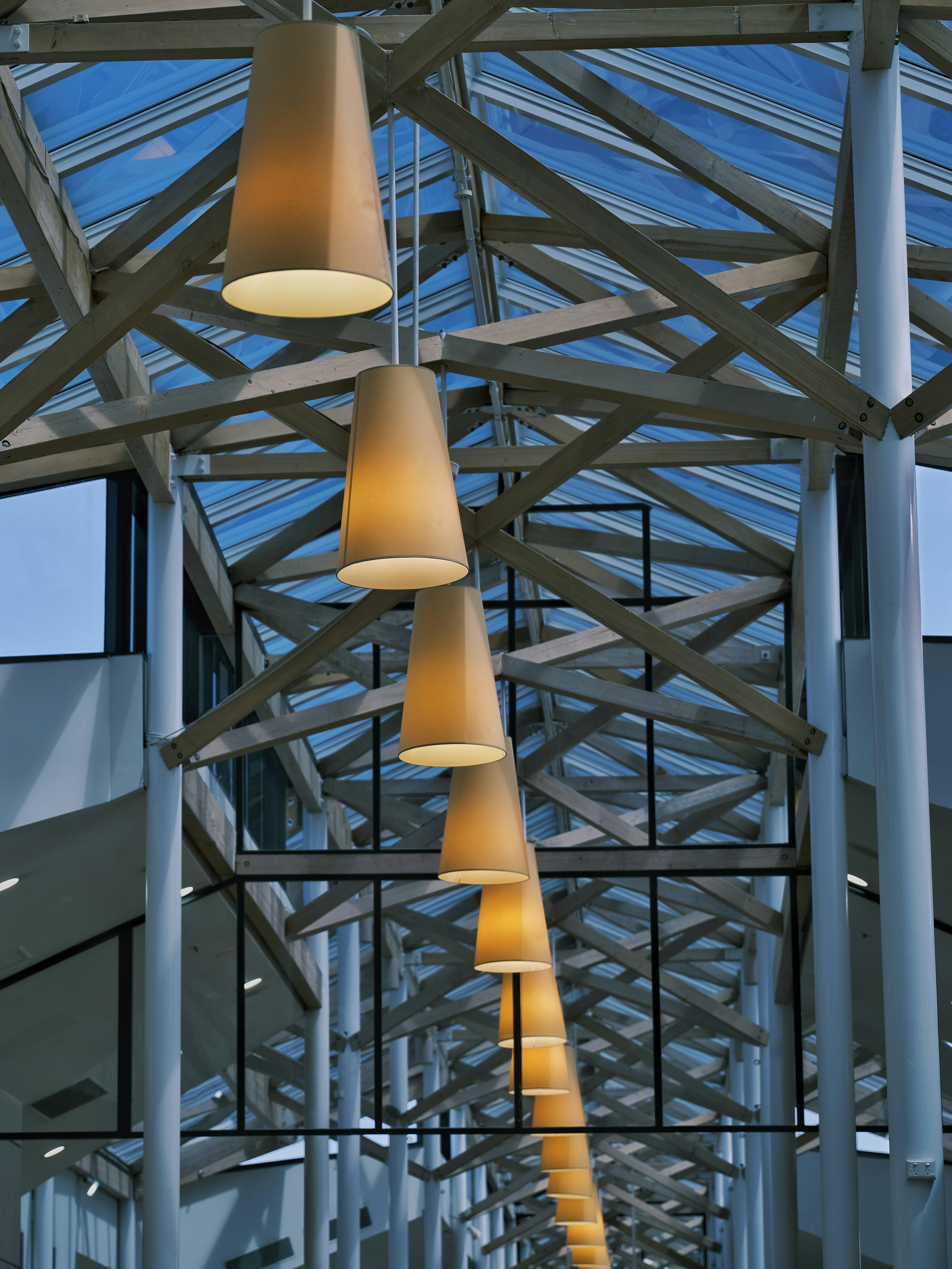 Row of warm pendant lamps marching through a glass-walled atrium