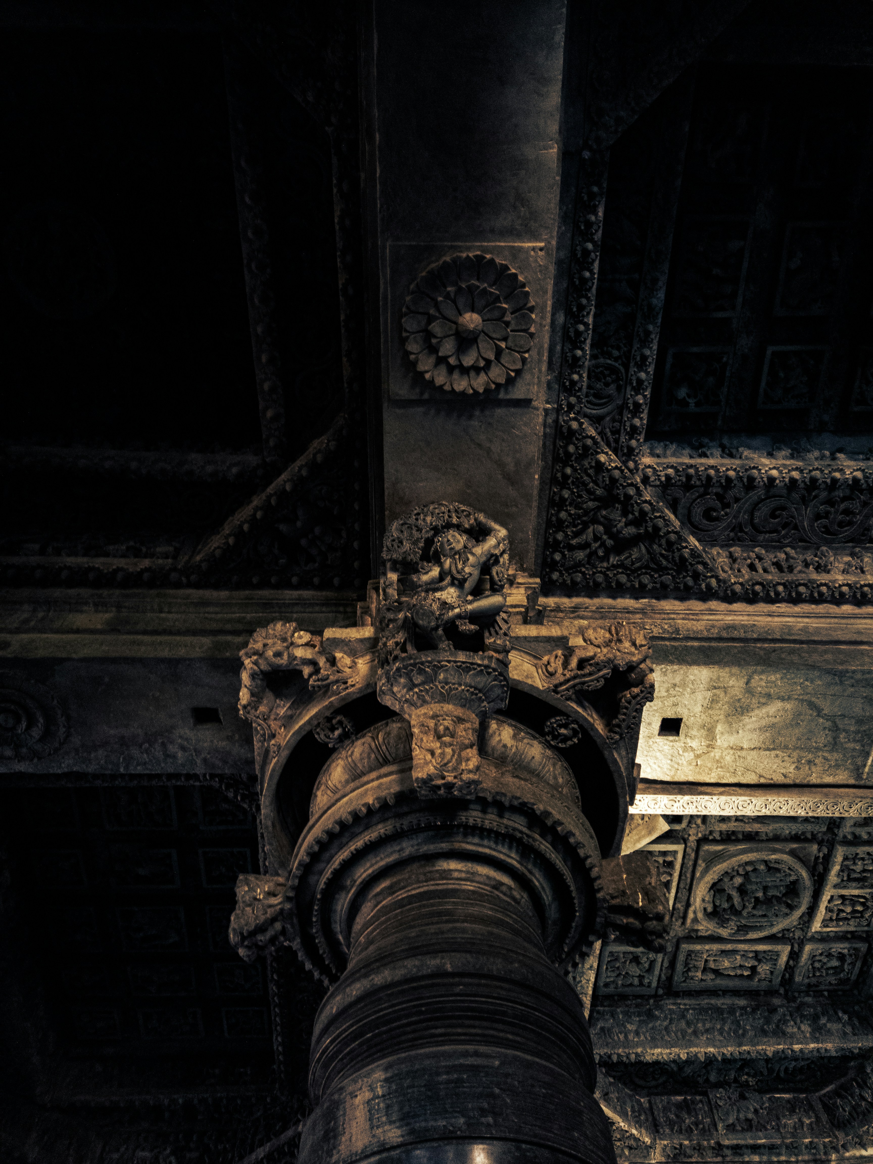 Intricately carved pillar and ceiling details in dark temple.