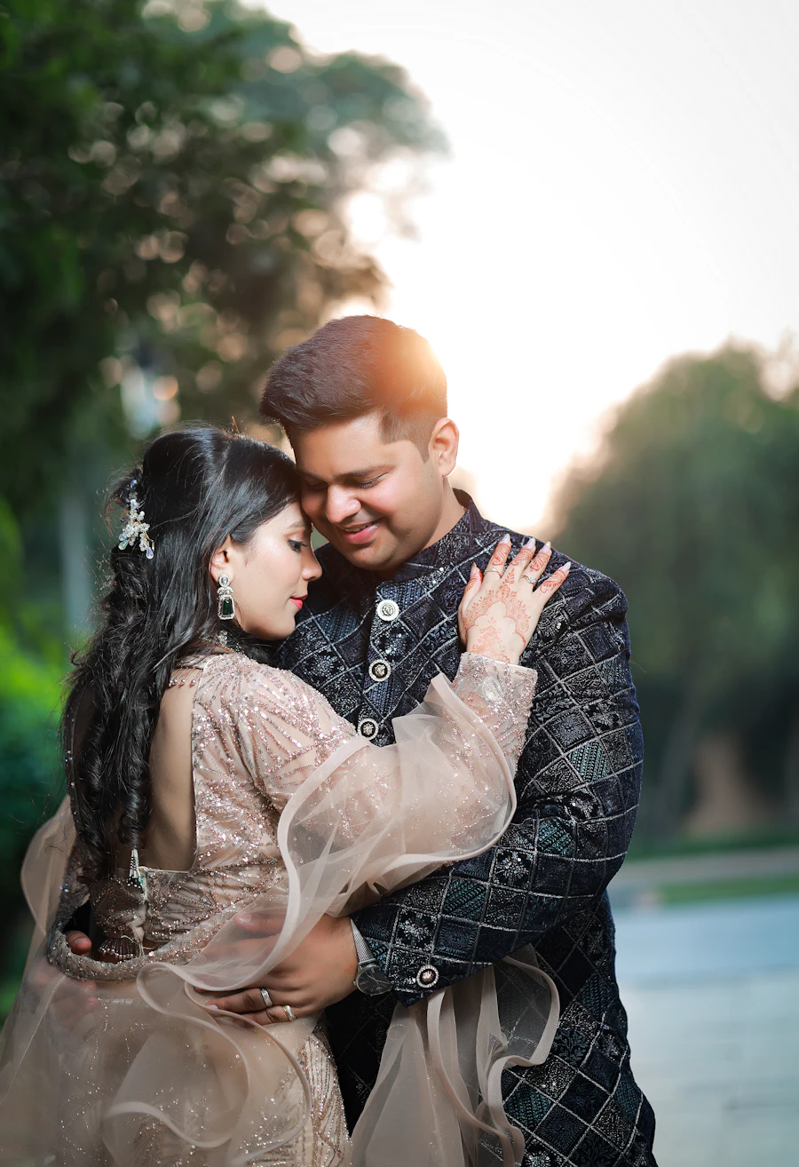 Two lovers embrace in soft, shimmering attire as warm sunset bleeds behind them, capturing an intimate portrait with gentle bokeh and textured fabrics.