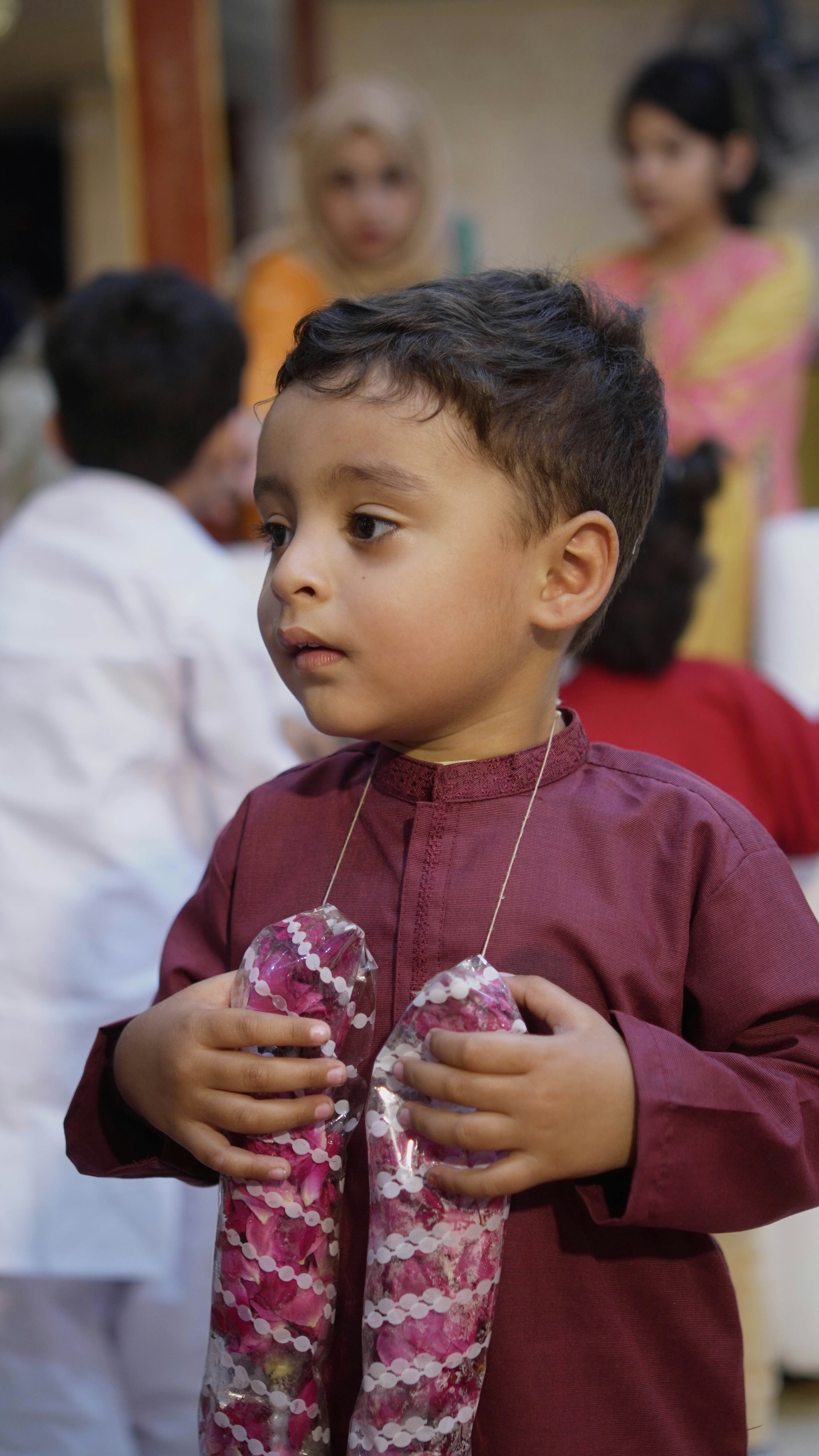 Child in maroon kurta holds decorative garlands at a festive gathering