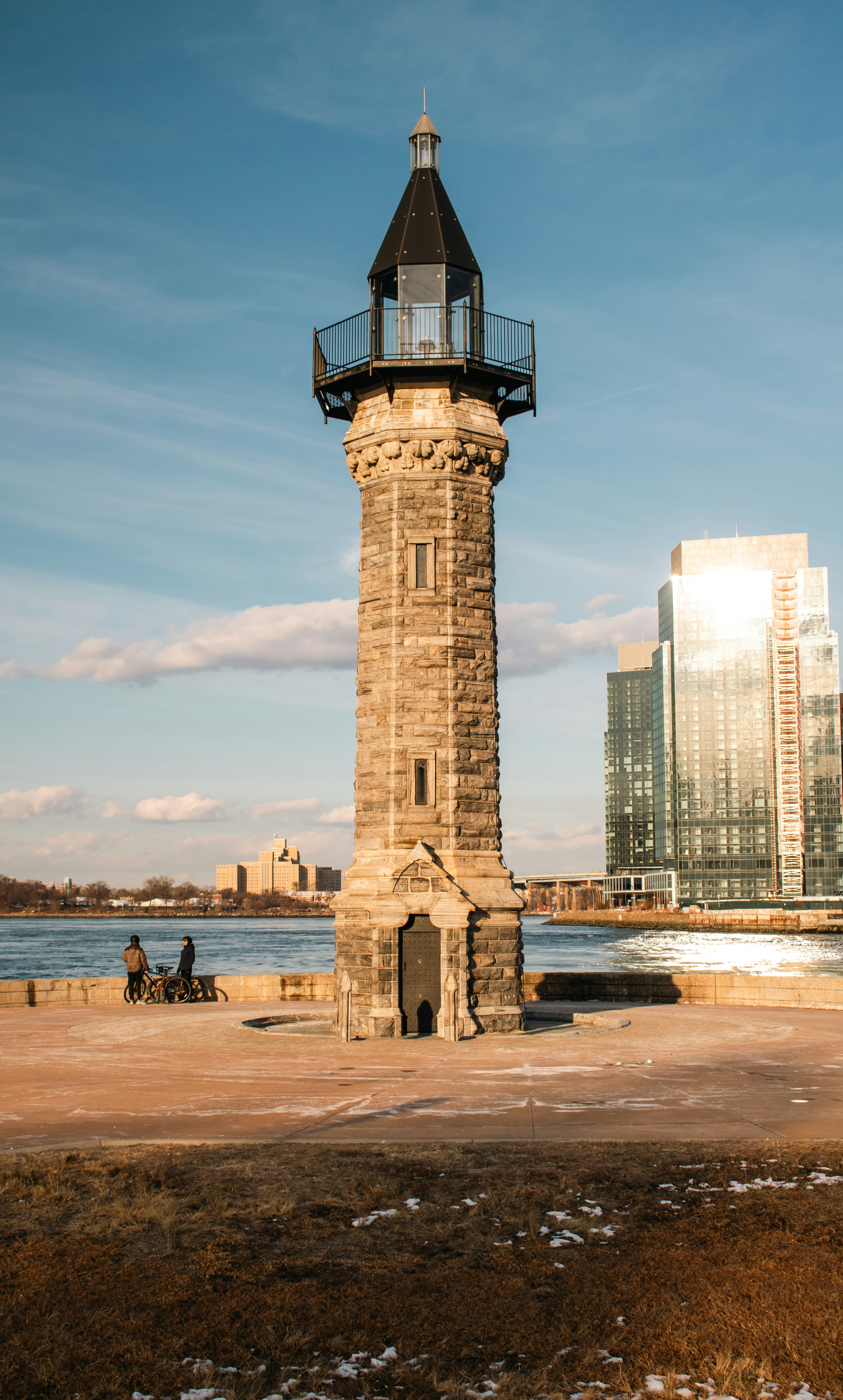 Beacon Amid Glassed Horizons: A Stone Lighthouse Straddling Water and Skyscrapers