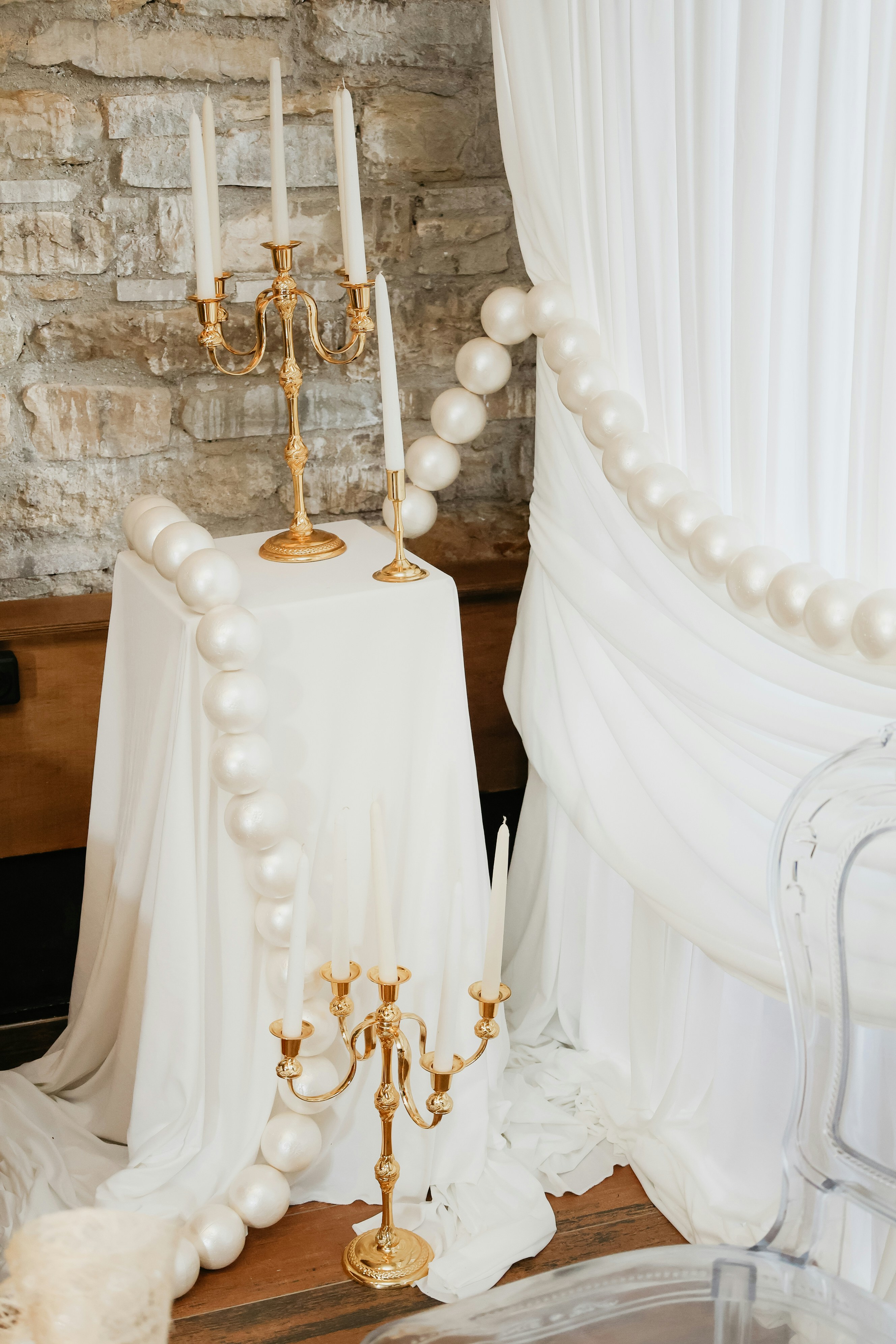 Elegant still life: draped white fabrics framing golden candelabras and a stone backdrop
