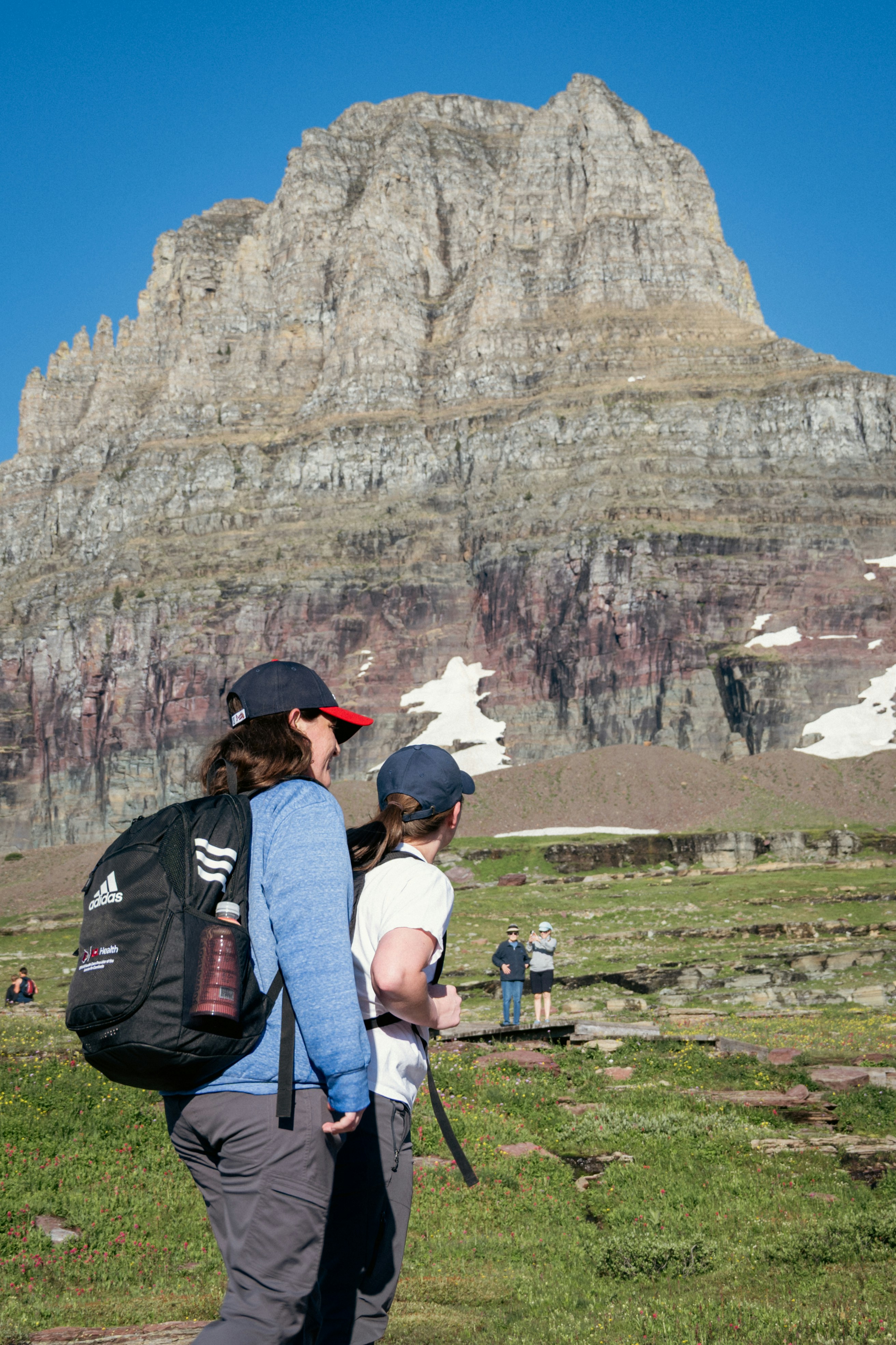 Two hikers in the shadow of a rugged cliff under a clear blue sky