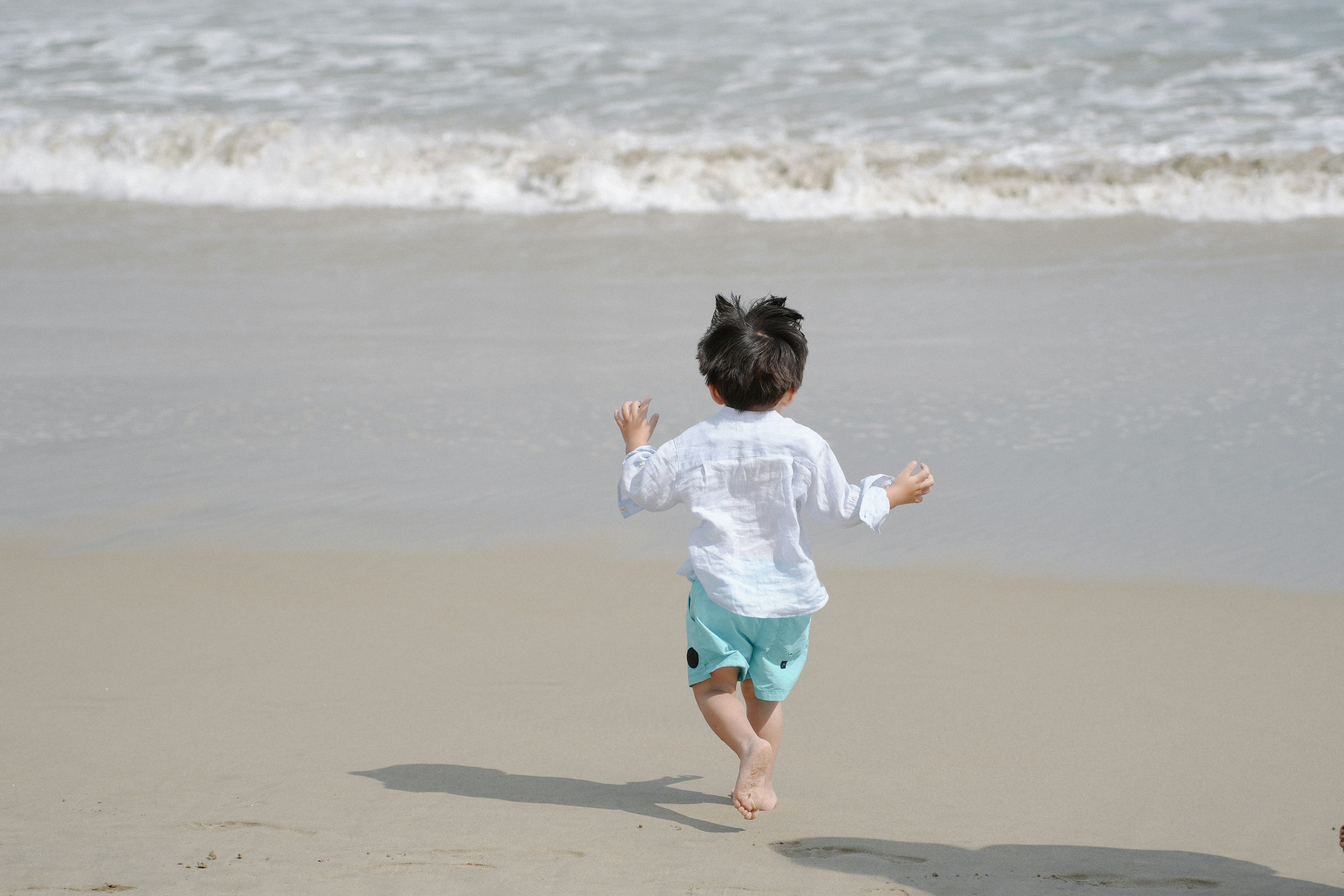 Young boy running towards the ocean waves.
