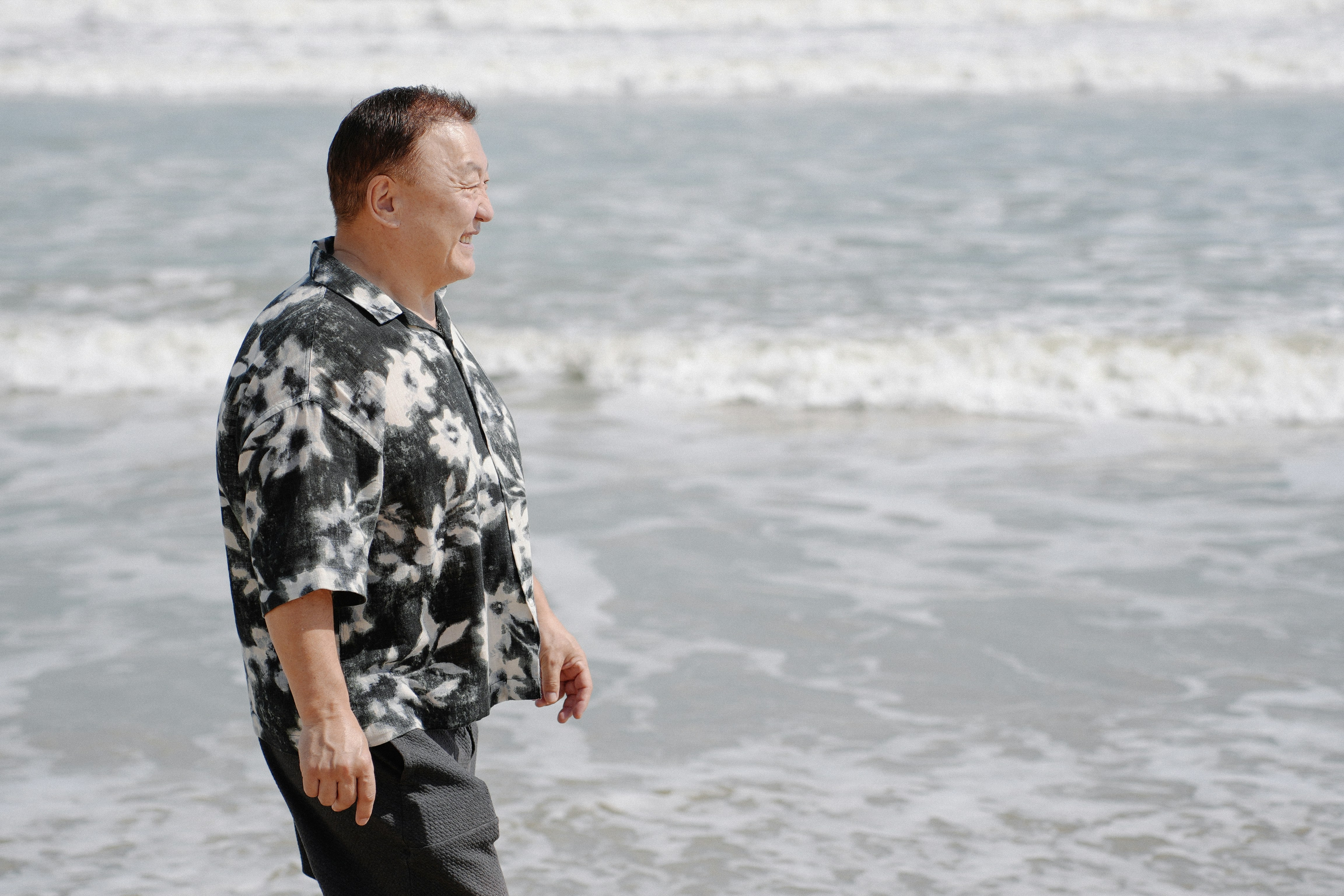 Man in hawaiian shirt walks by the ocean waves