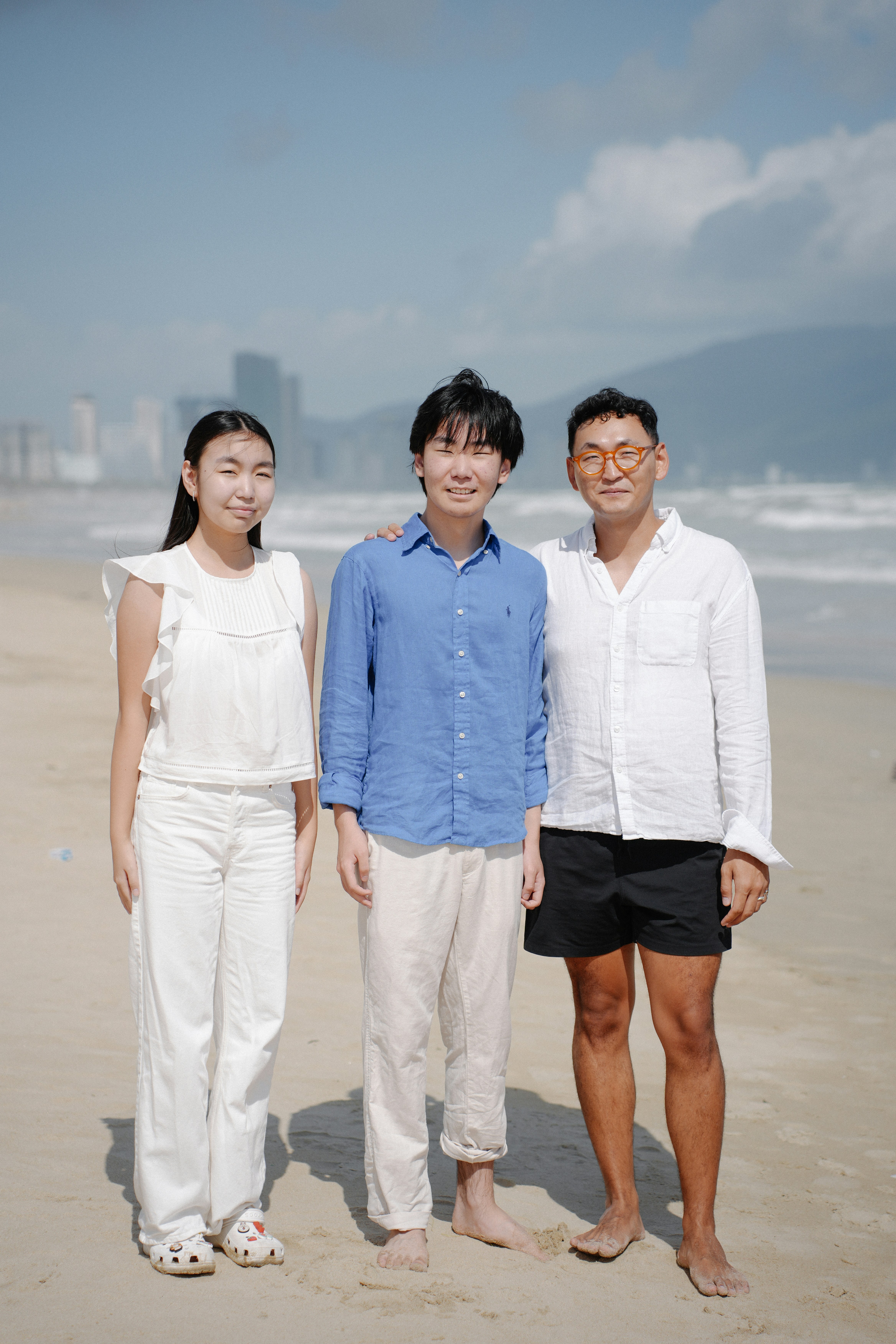 Three people standing on a sandy beach.