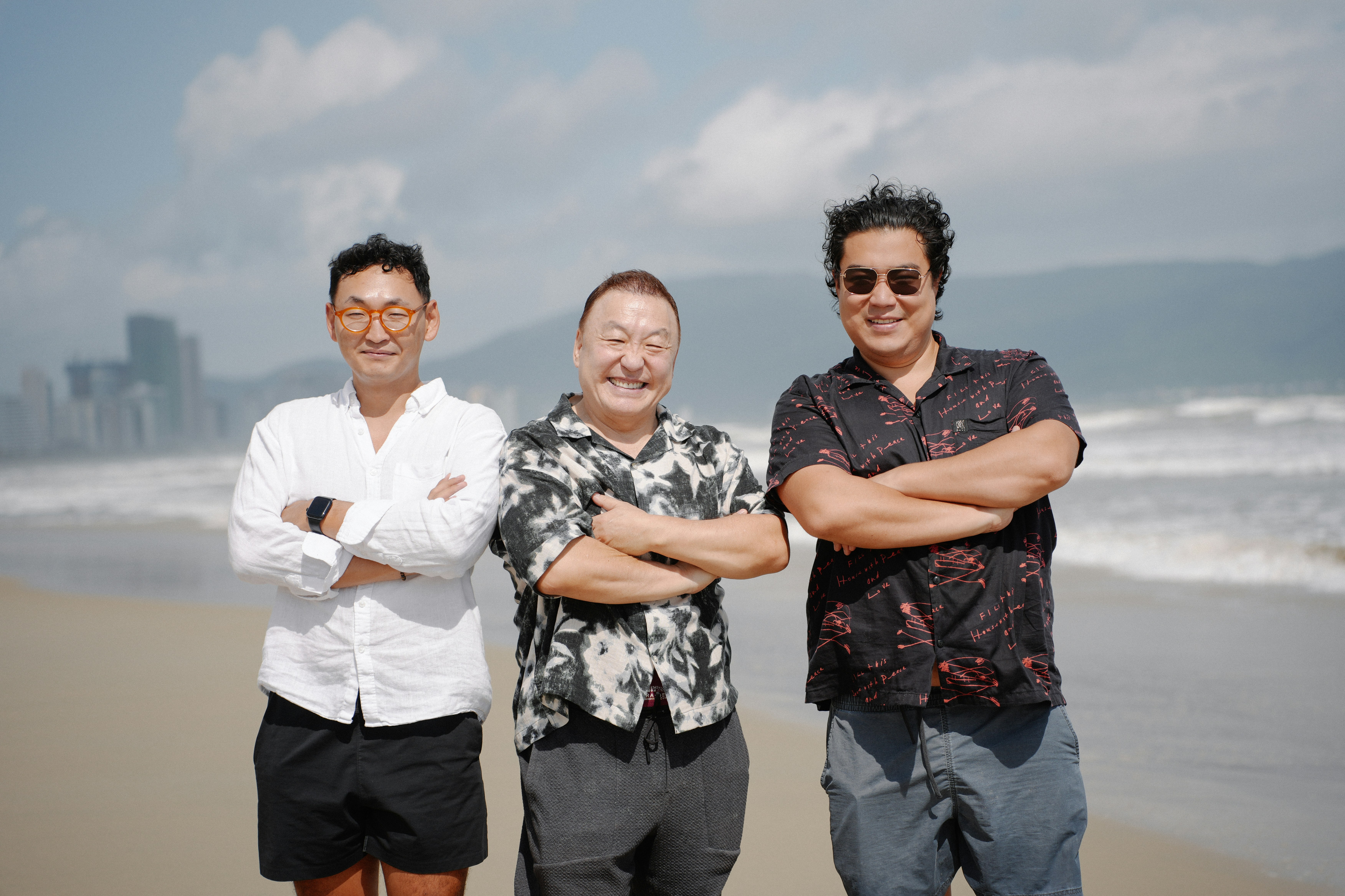 Three men posing on a beach with arms crossed
