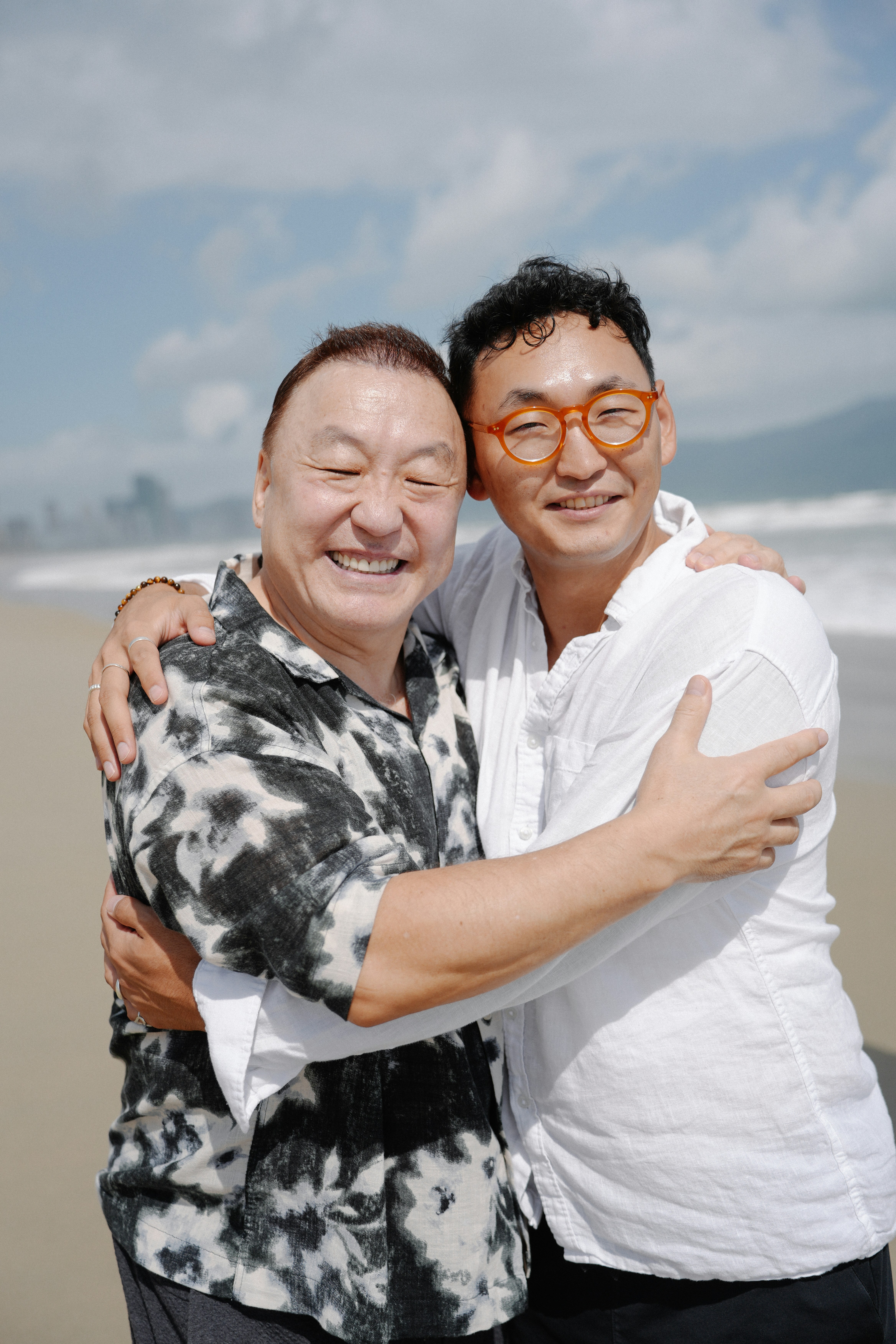 Two smiling men hugging on a beach.