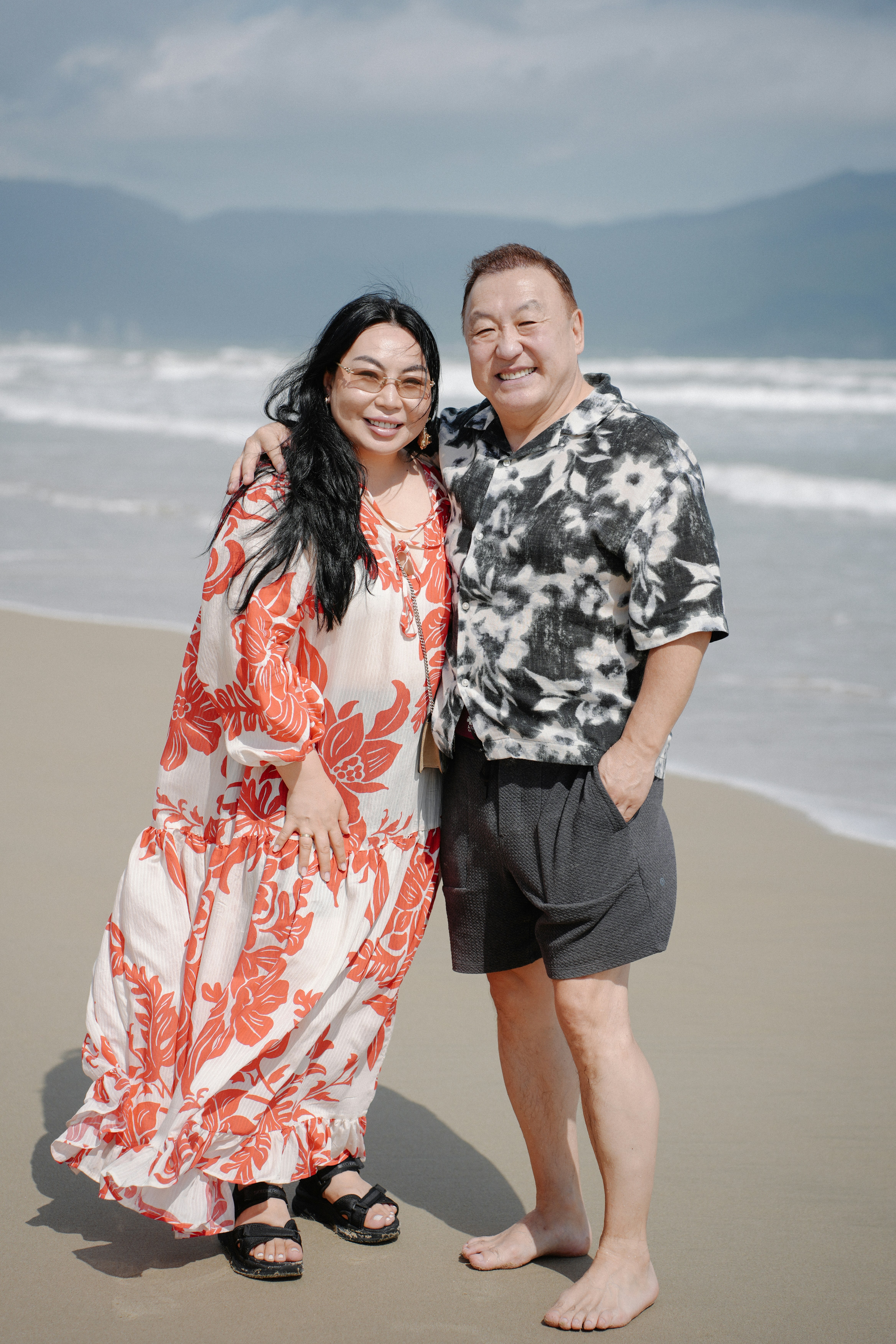 Couple posing on a sunny beach with ocean waves.