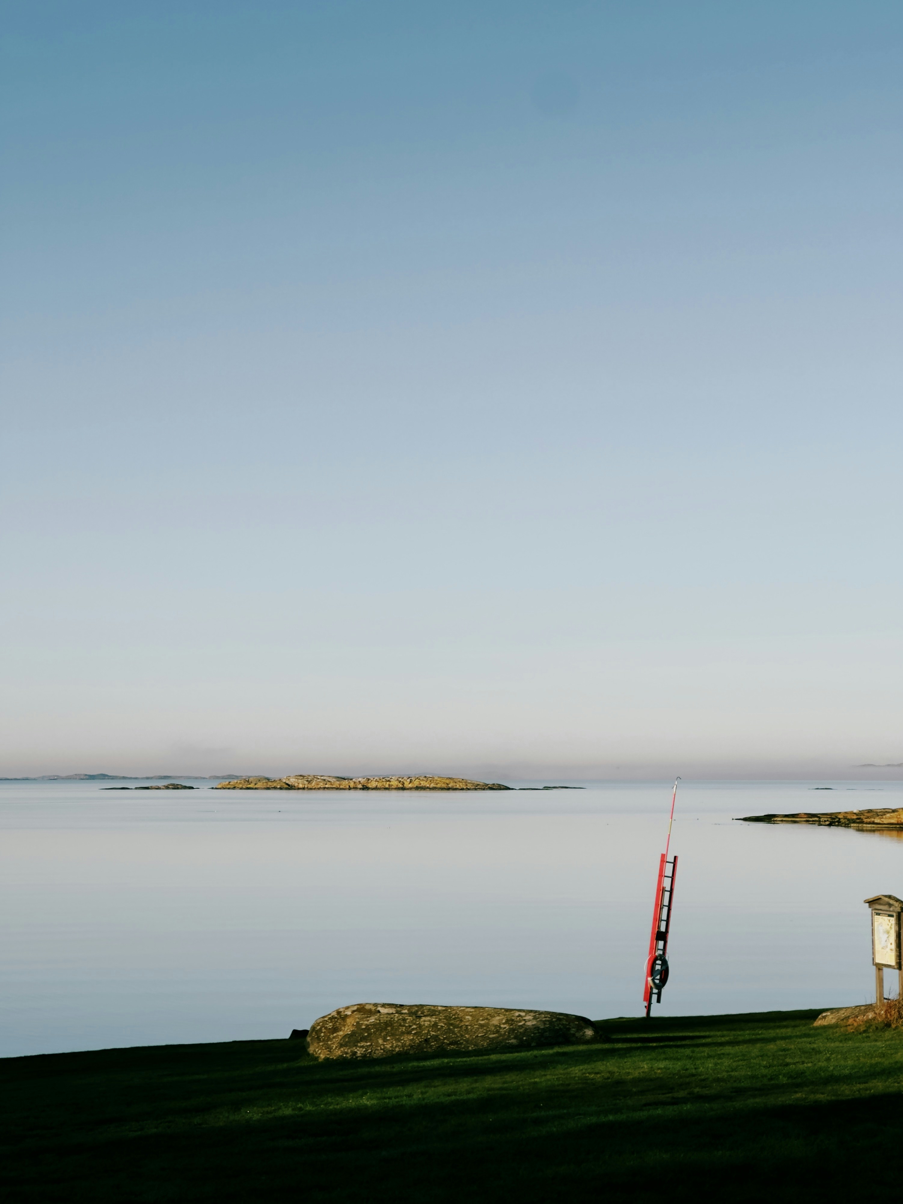 Lone flagpole by the calm shoreline at dusk