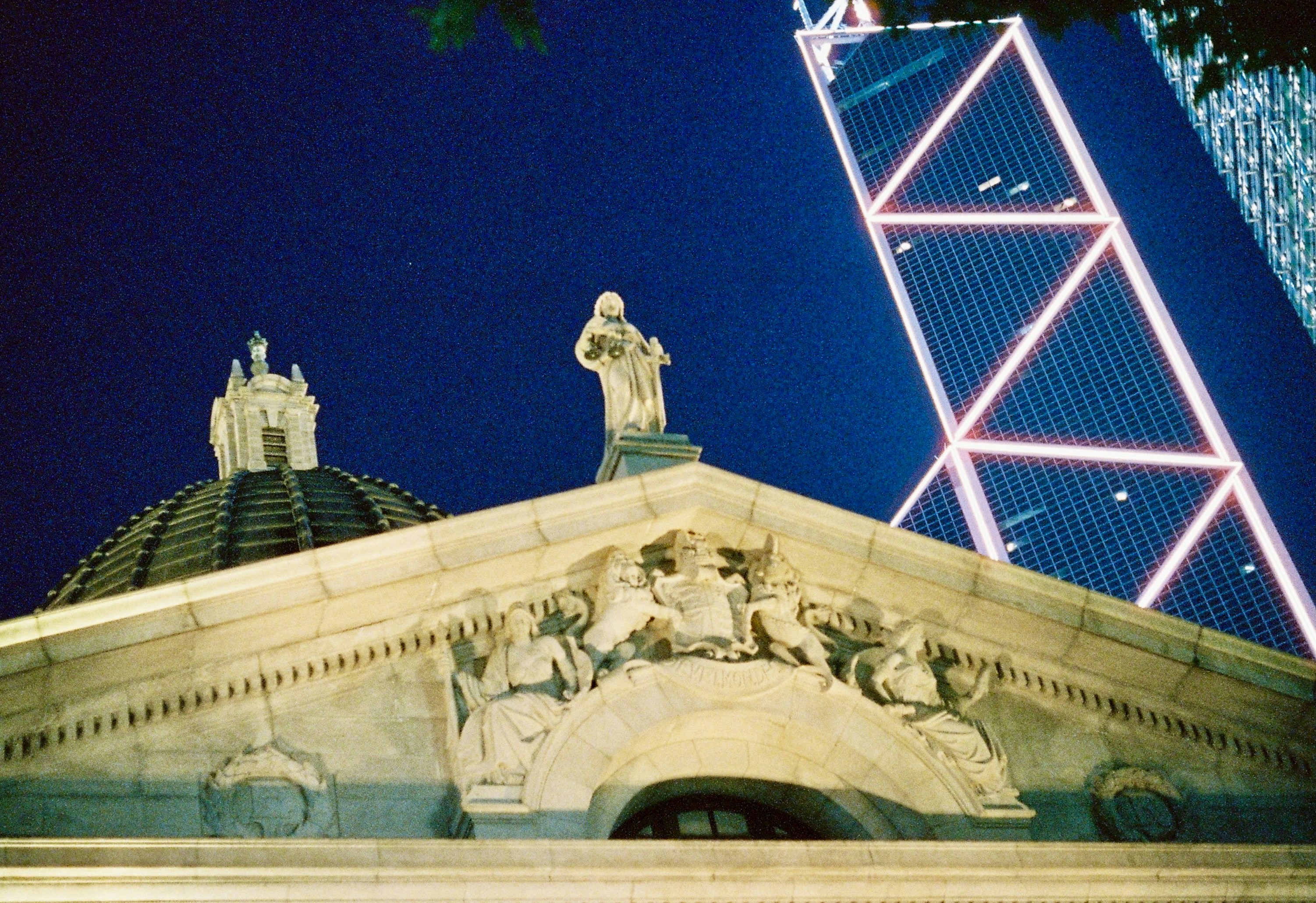 Nighttime Pediment: Statues Overlook a Neon-Outlined Skyscraper
