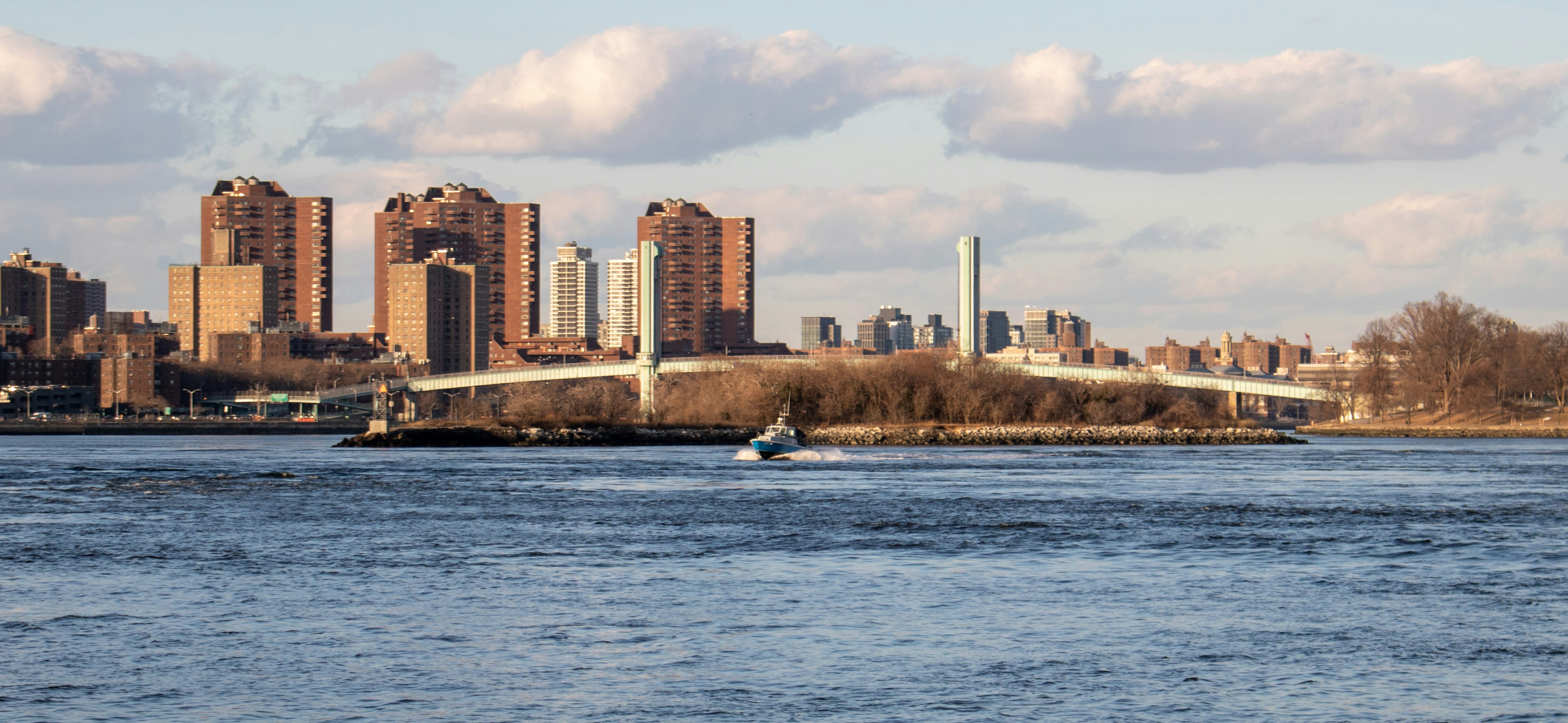 A photograph of the Wards Island Bridge, also known as the 103rd Street Footbridge, spanning the Harlem River in New York City. The image shows a pedestrian and bicycle vertical lift bridge connecting Manhattan at East 103rd Street with Wards Island. Opened in 1951, the bridge features a central lift span designed to rise for river traffic. It can be used for topics related to urban infrastructure, pedestrian bridges, transportation history, river crossings, city planning, and everyday movement within New York City.
