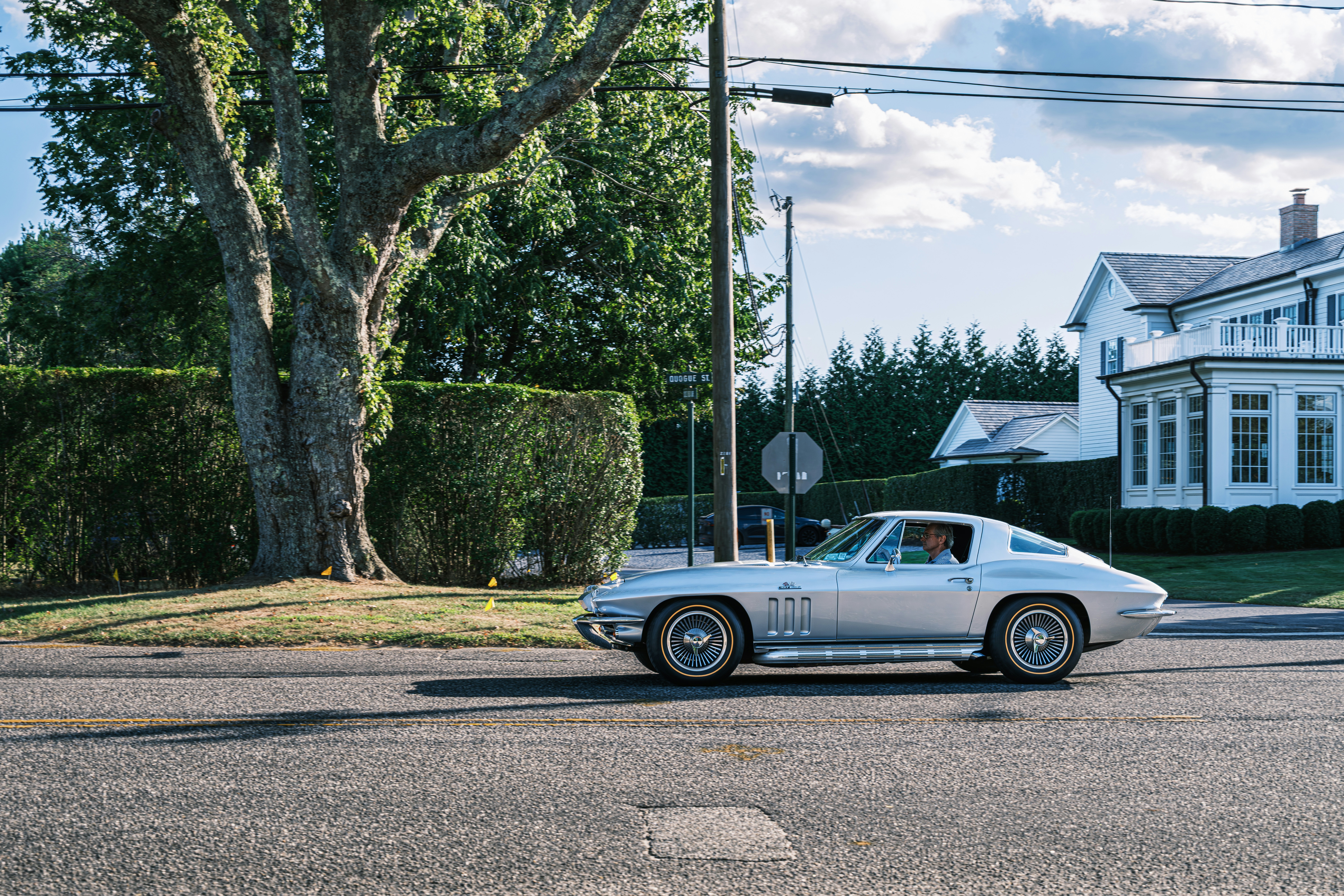 A classic Chevrolet Corvette driven along a residential street in Quogue, New York, showcasing vintage American sports car design.