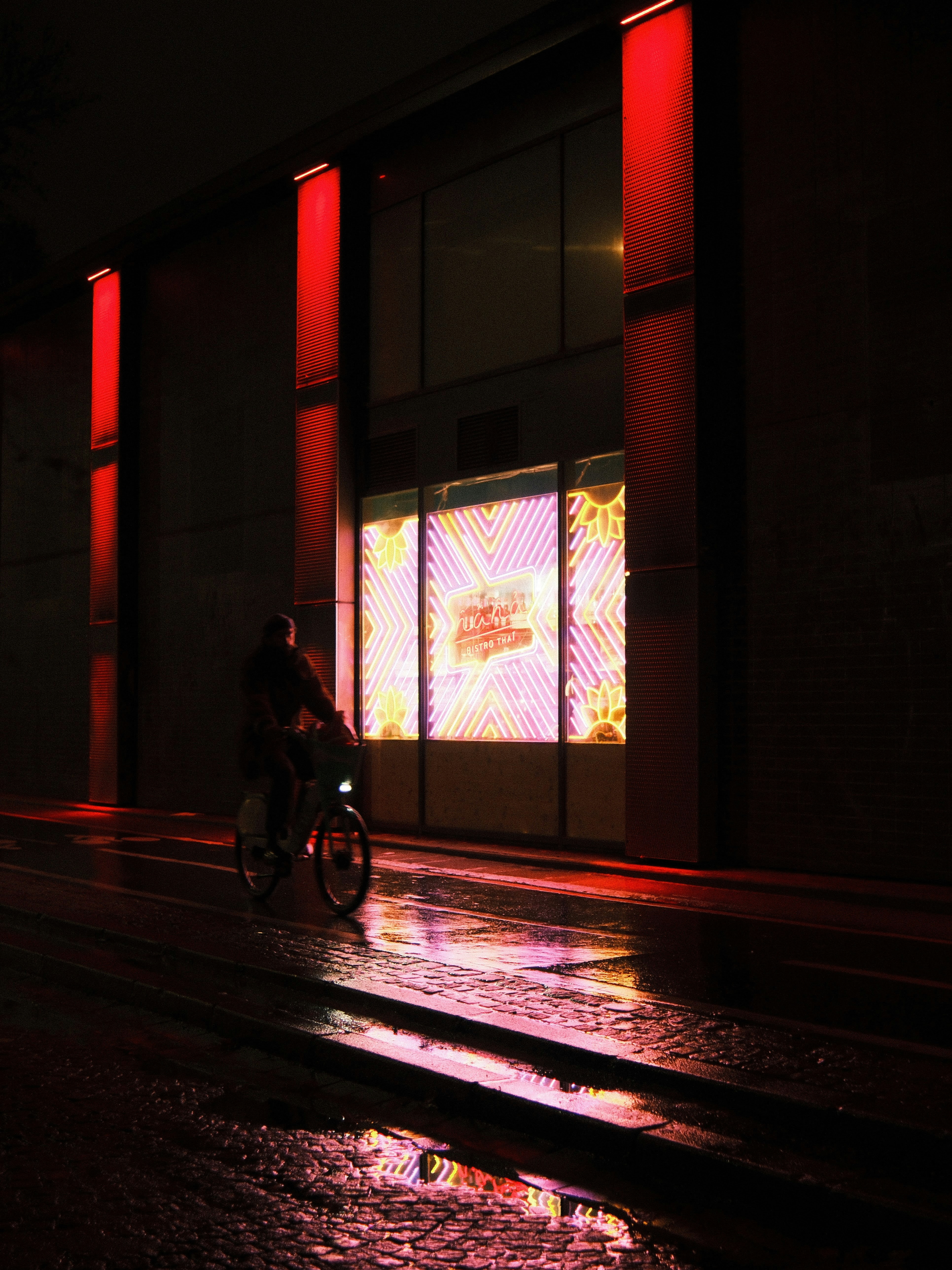 Neon Ride Through Rain: A Night Bicycle in Front of Lit Windows