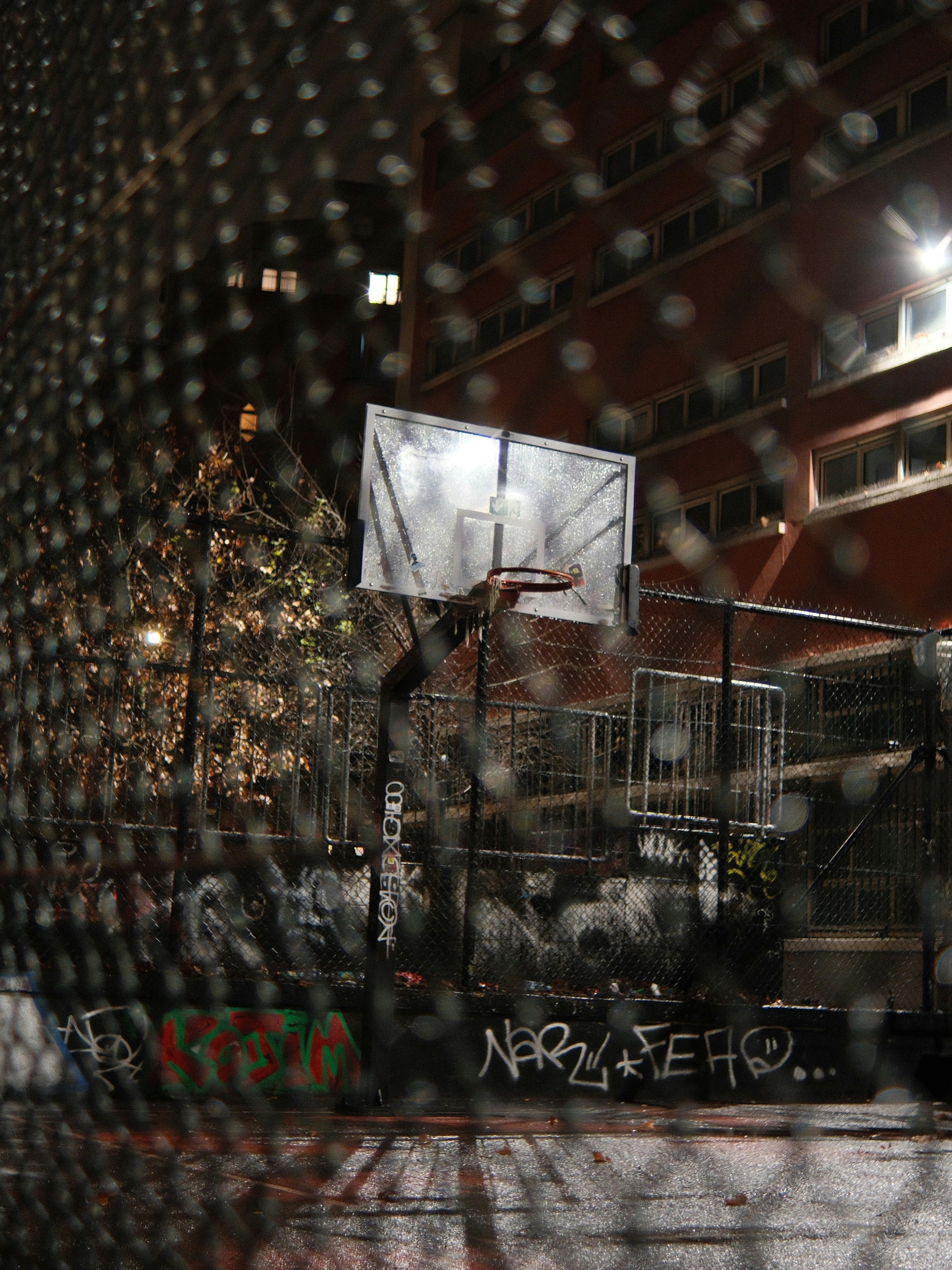 Basketball Hoop Behind a Wet City Fence at Night