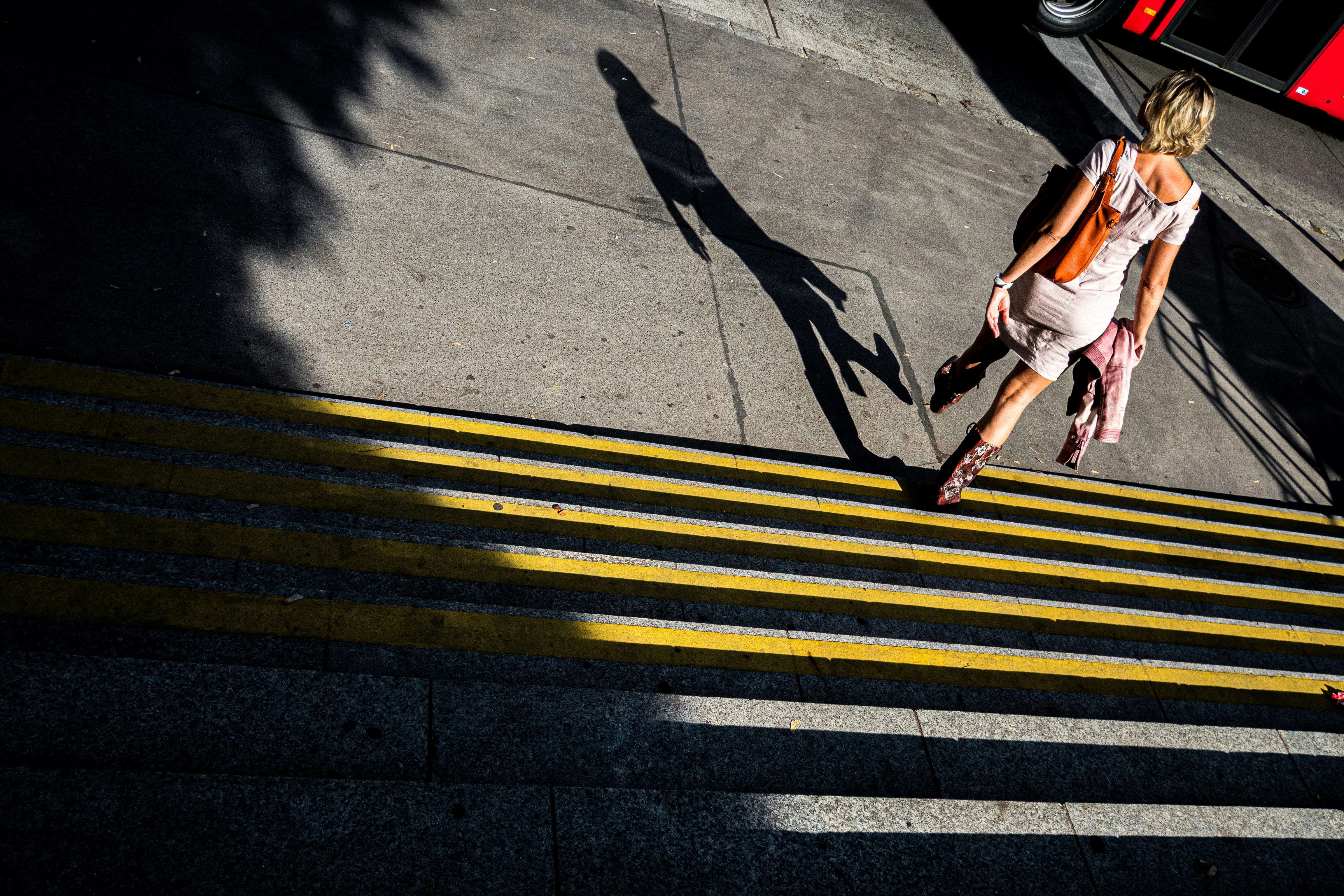 Pedestrian stride on a sunlit crosswalk casts a long shadow