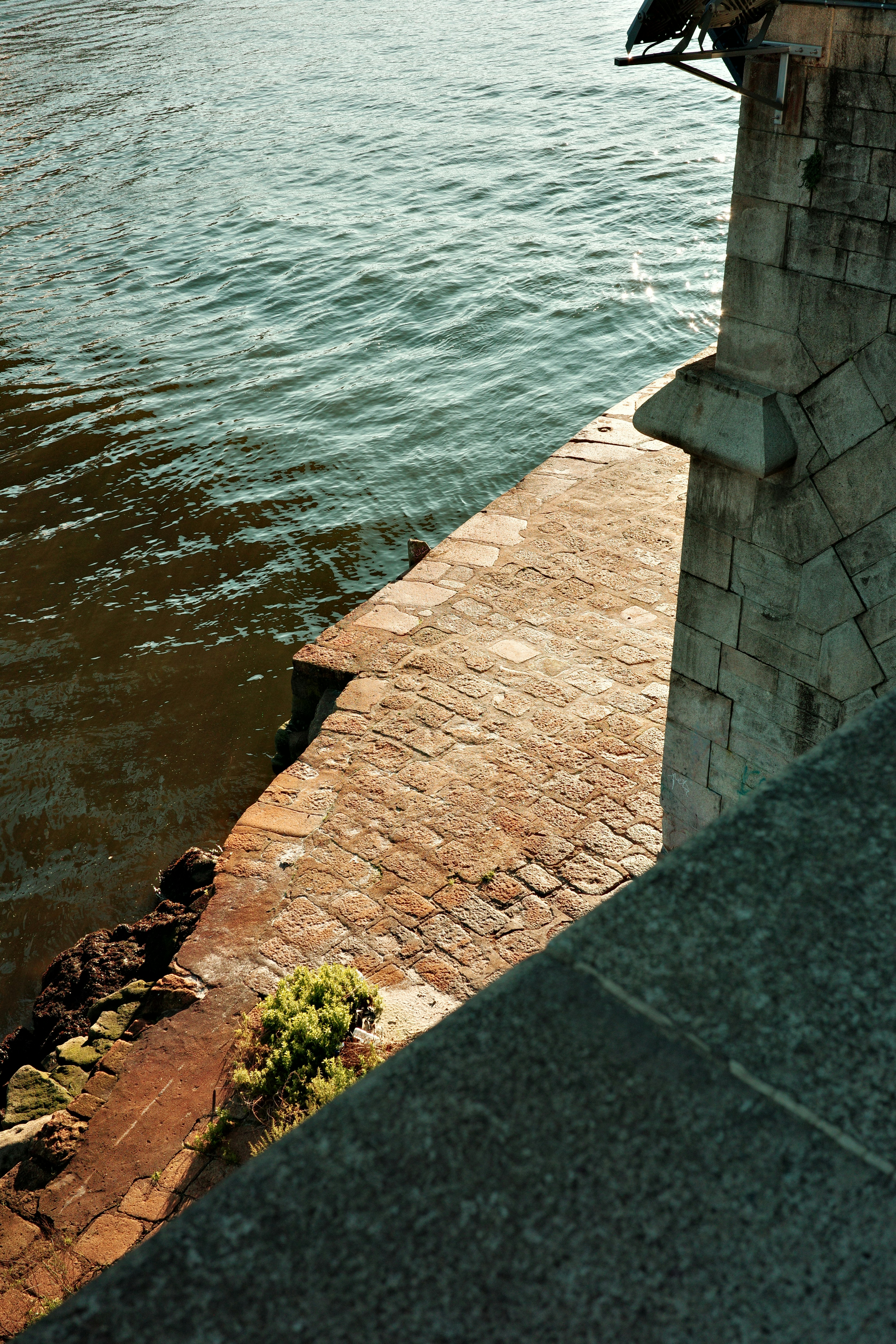 Stone Pier Slopes into Quiet River, with Towered Wall Casting Shadow
